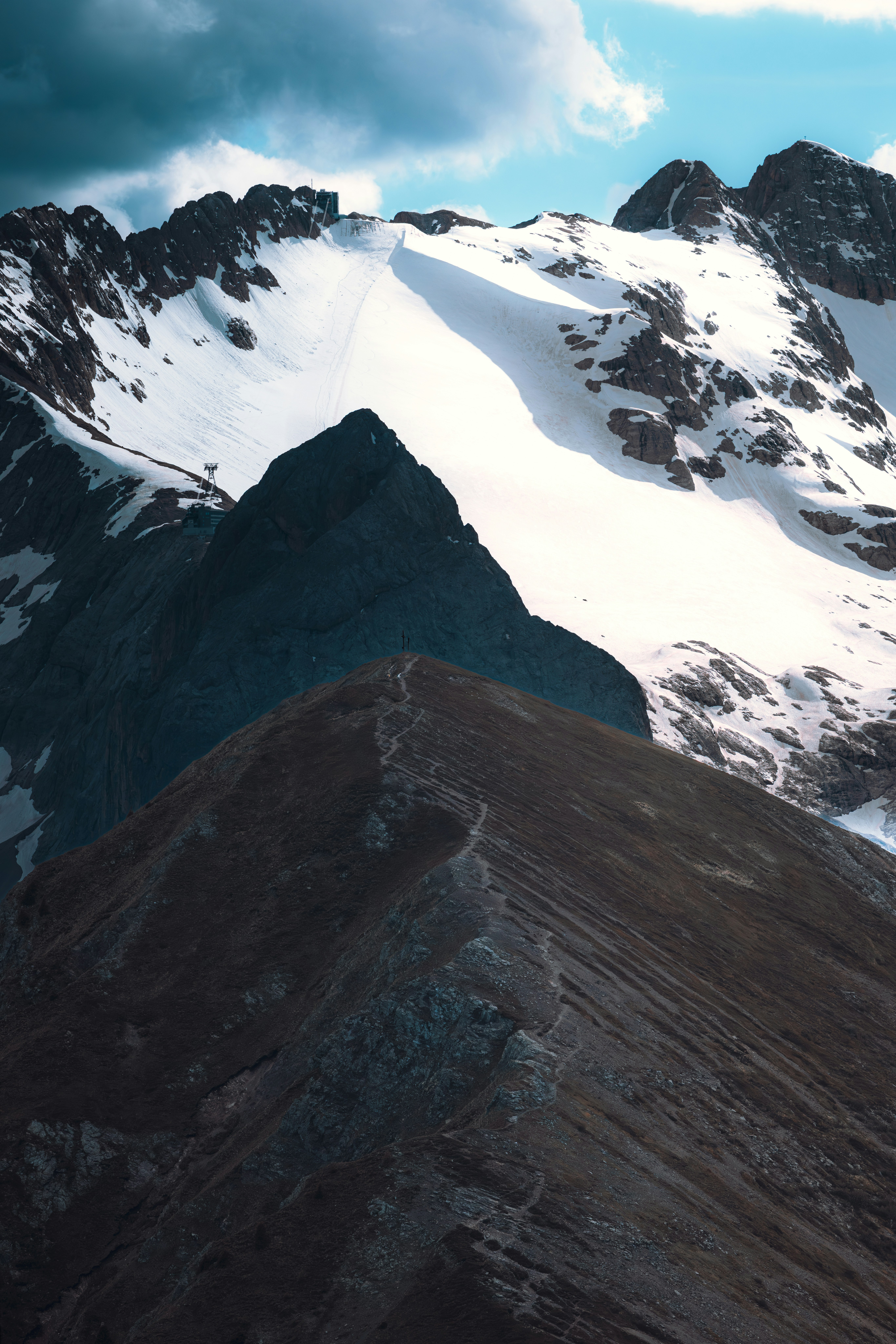 Snow-capped mountains and a rocky ridge under a cloudy sky.