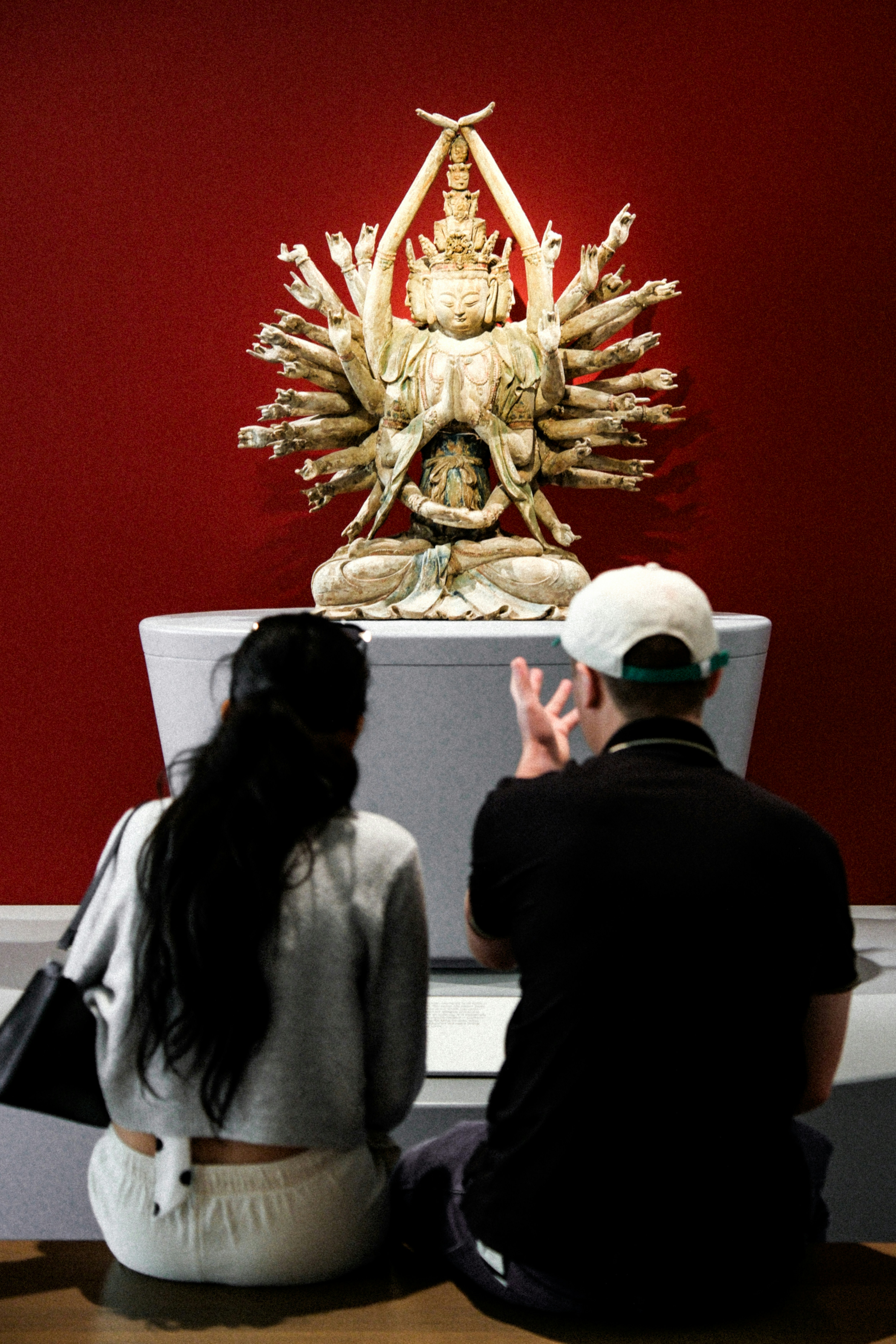 Two Visitors in Quiet Reverence Before a Multi-armed Sacred Sculpture