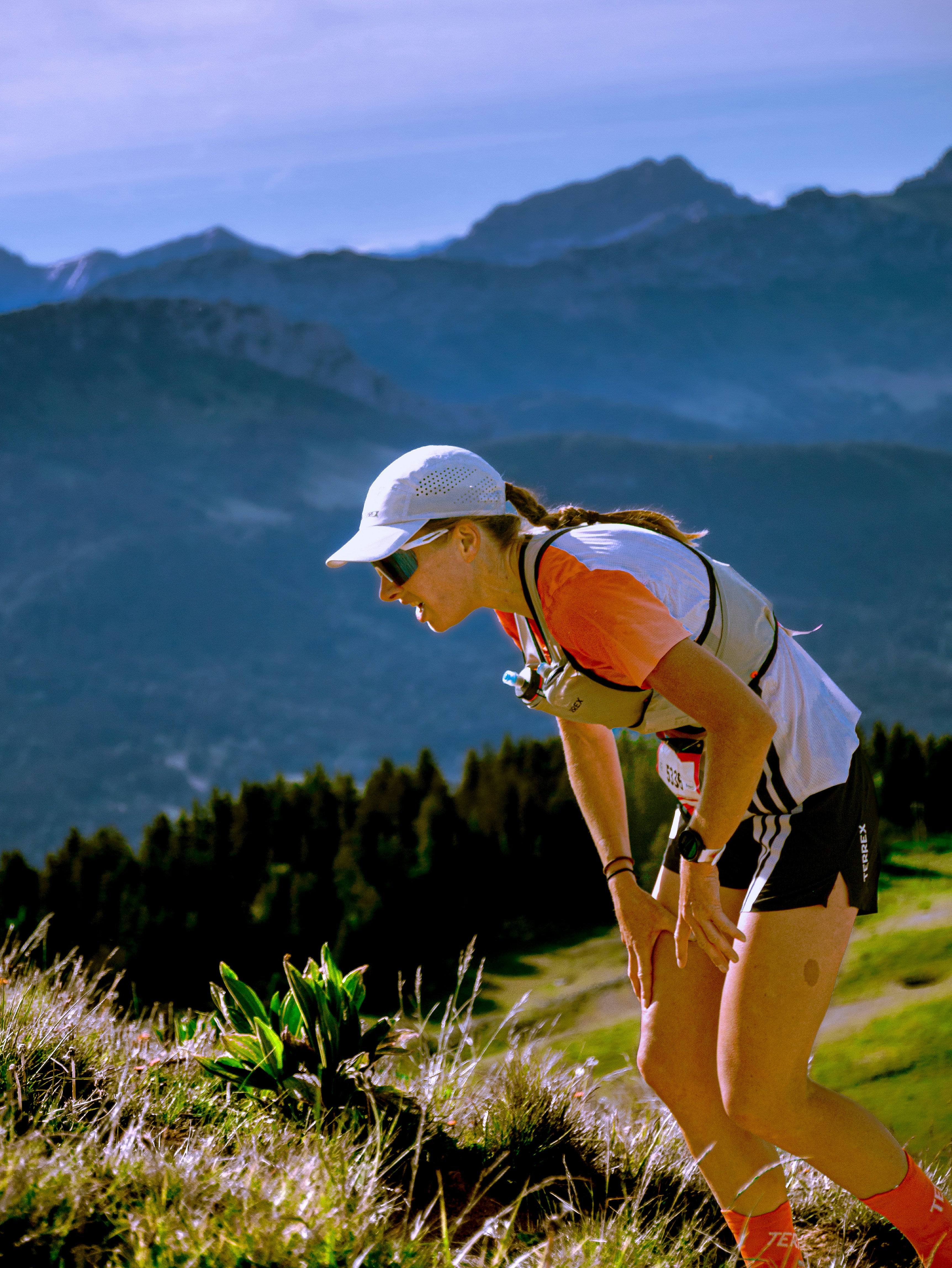 Sunlit Trail Runner Descends a Grassy Slope Under Alpine Peaks