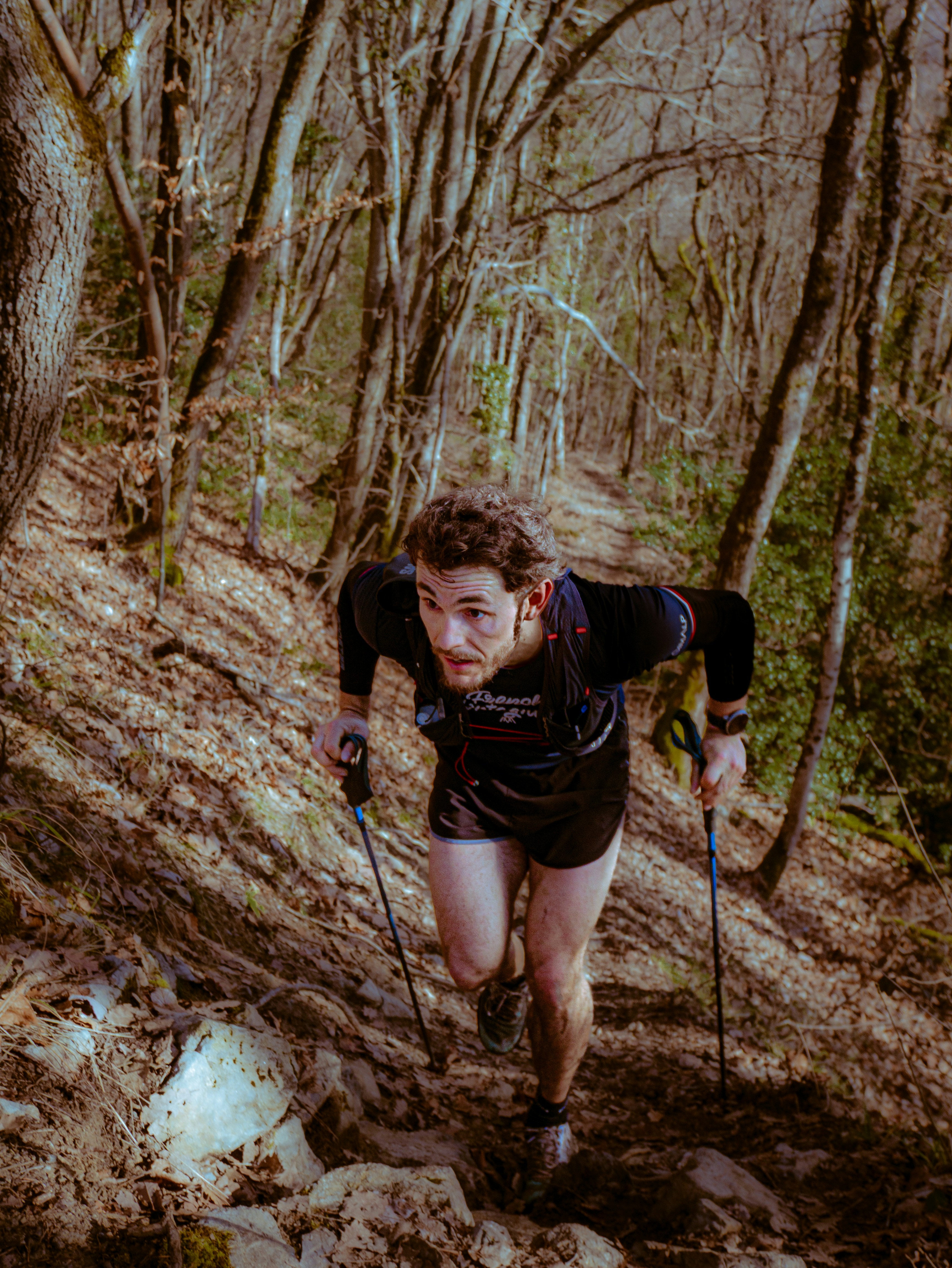 Athlete trail running uphill through a dense, barren forest.