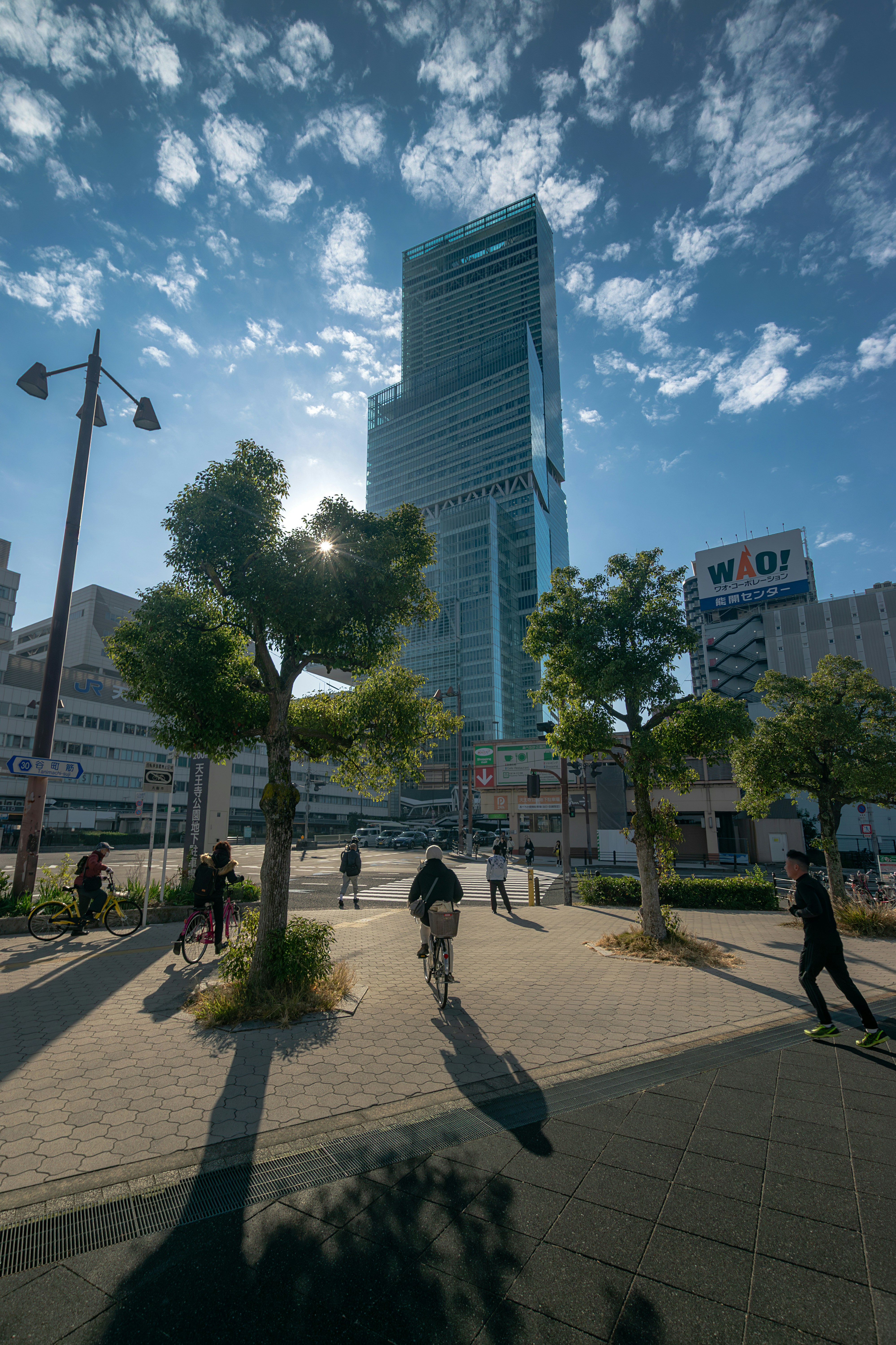 City Tower Ascends: Sunlit Street-Level Pulse Beneath a Sky-Scattered Canopy