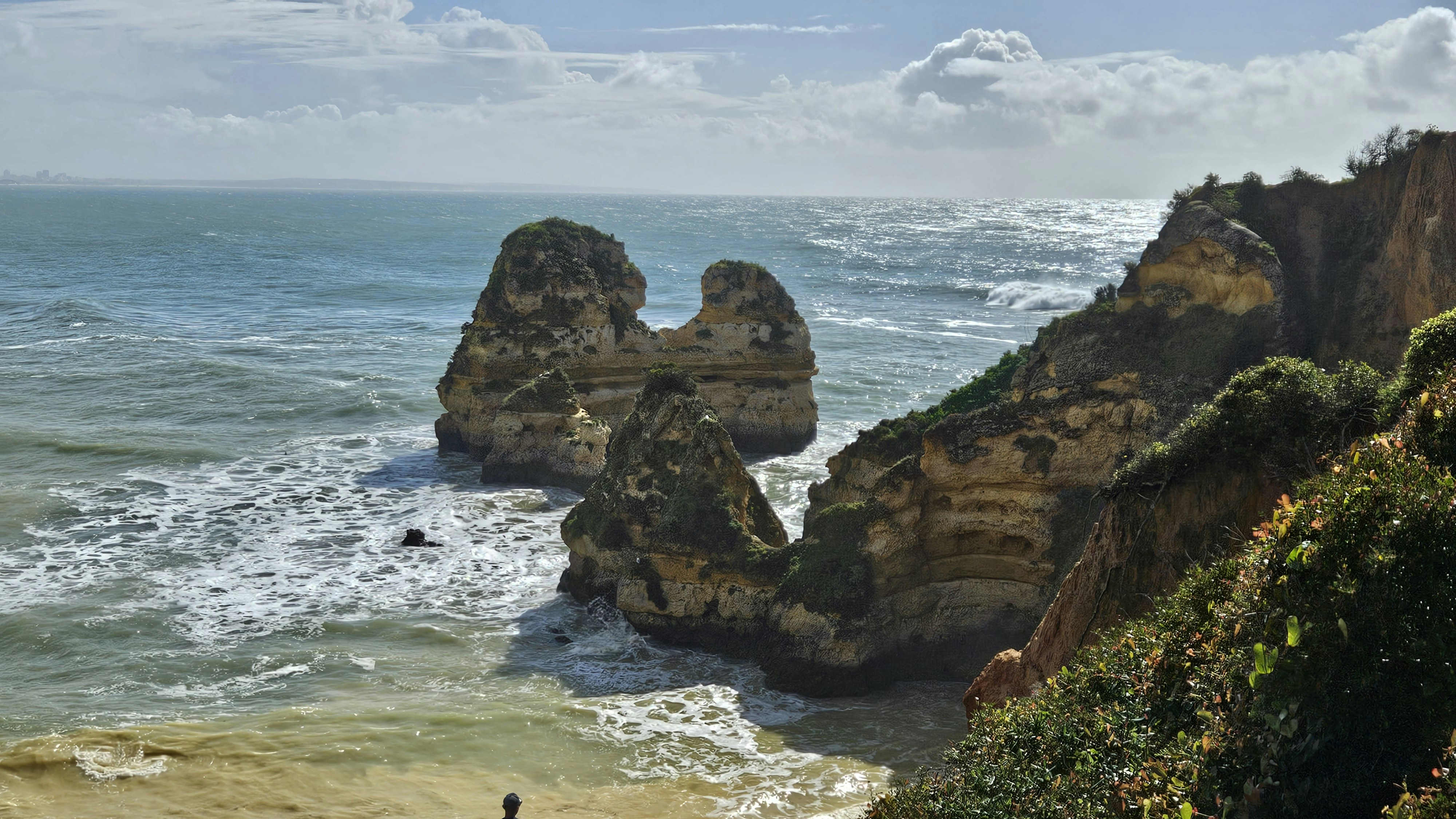 Coastal rock formations overlook the Atlantic with gentle surf and a sunlit cliffside panorama.