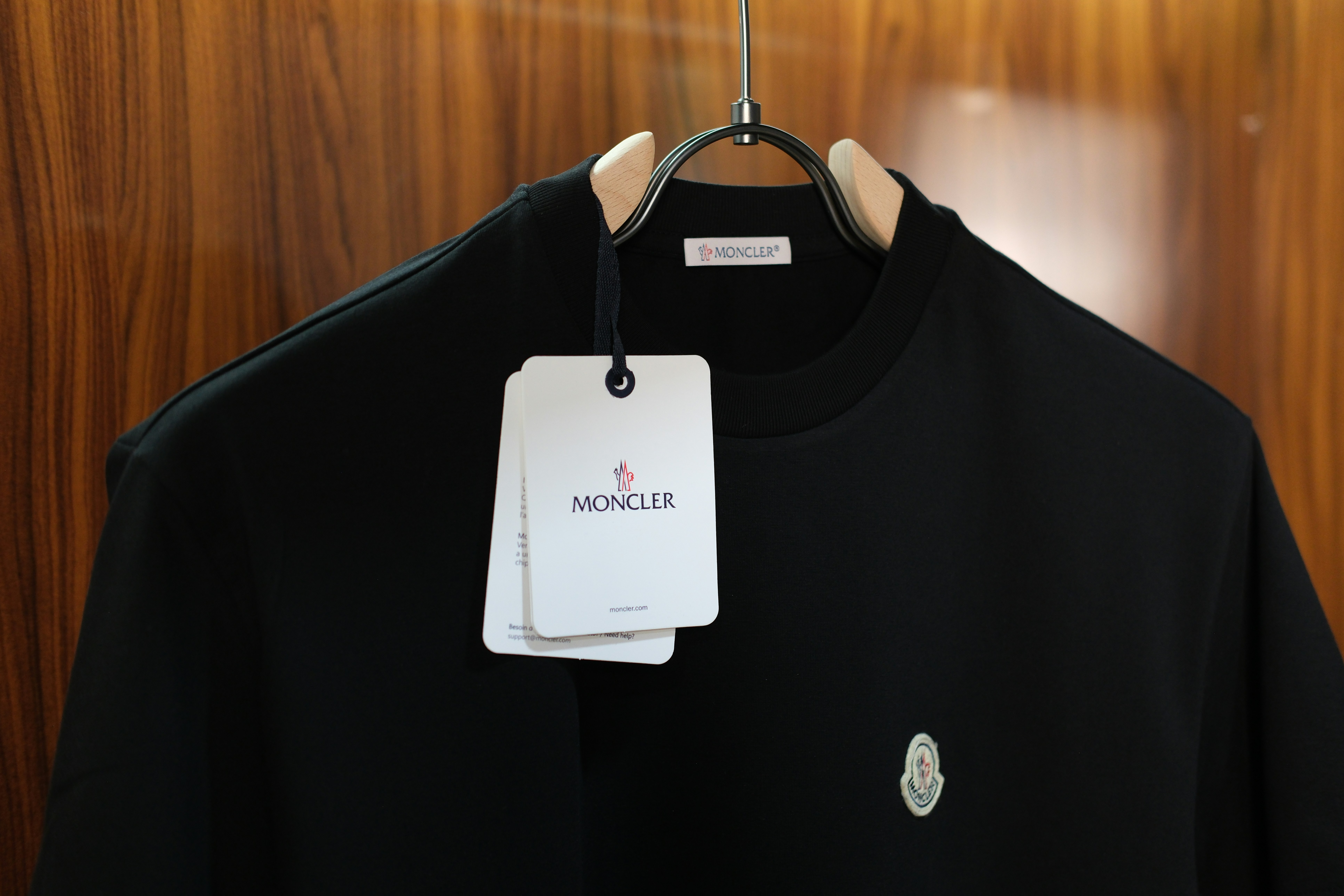 Black moncler sweatshirt with tags on a wooden hanger.