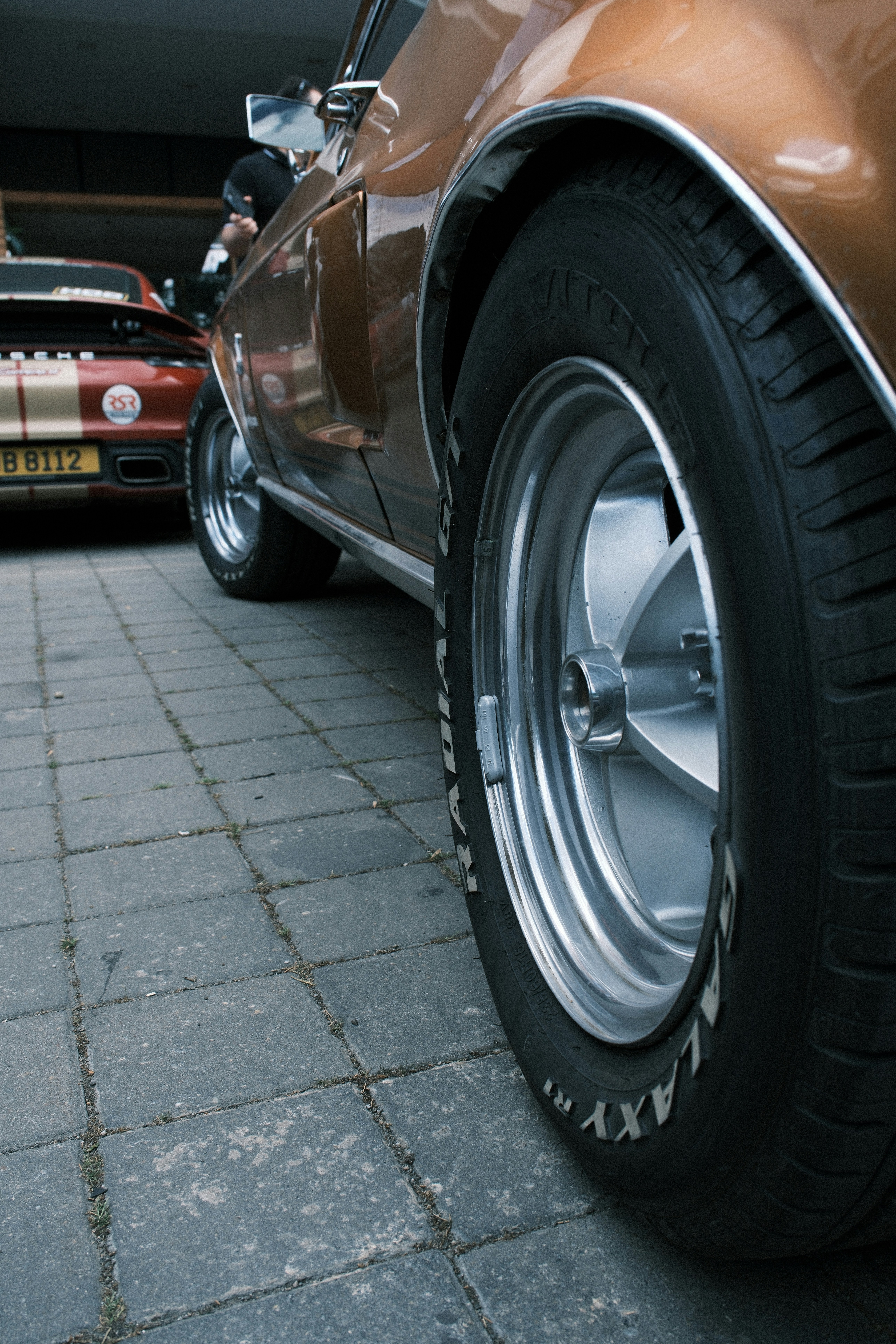 Classic car's wheel and tire parked on a brick surface.