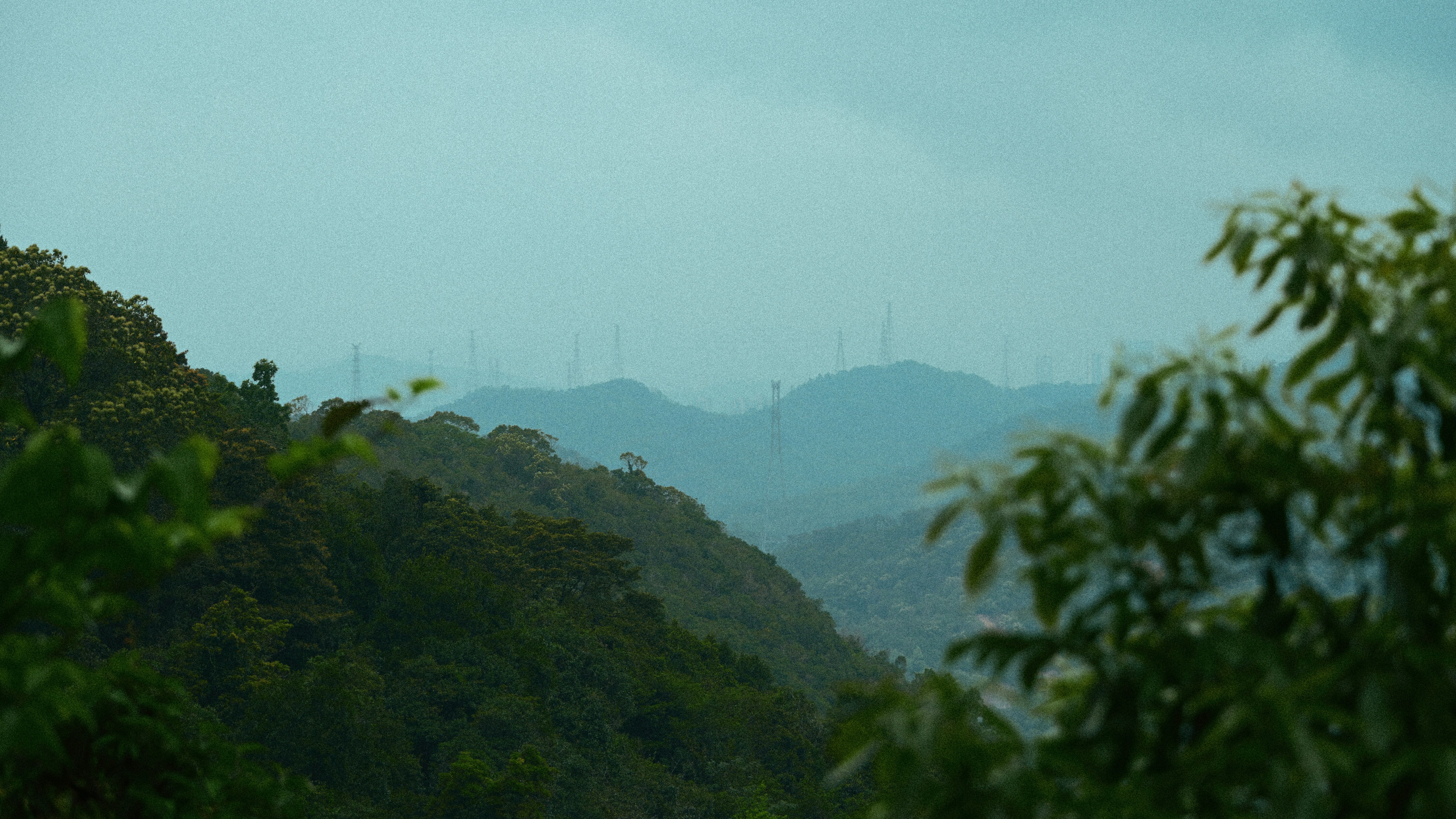 Hazy Ridgeline: Distant Wind Turbines Beyond Lush Hills