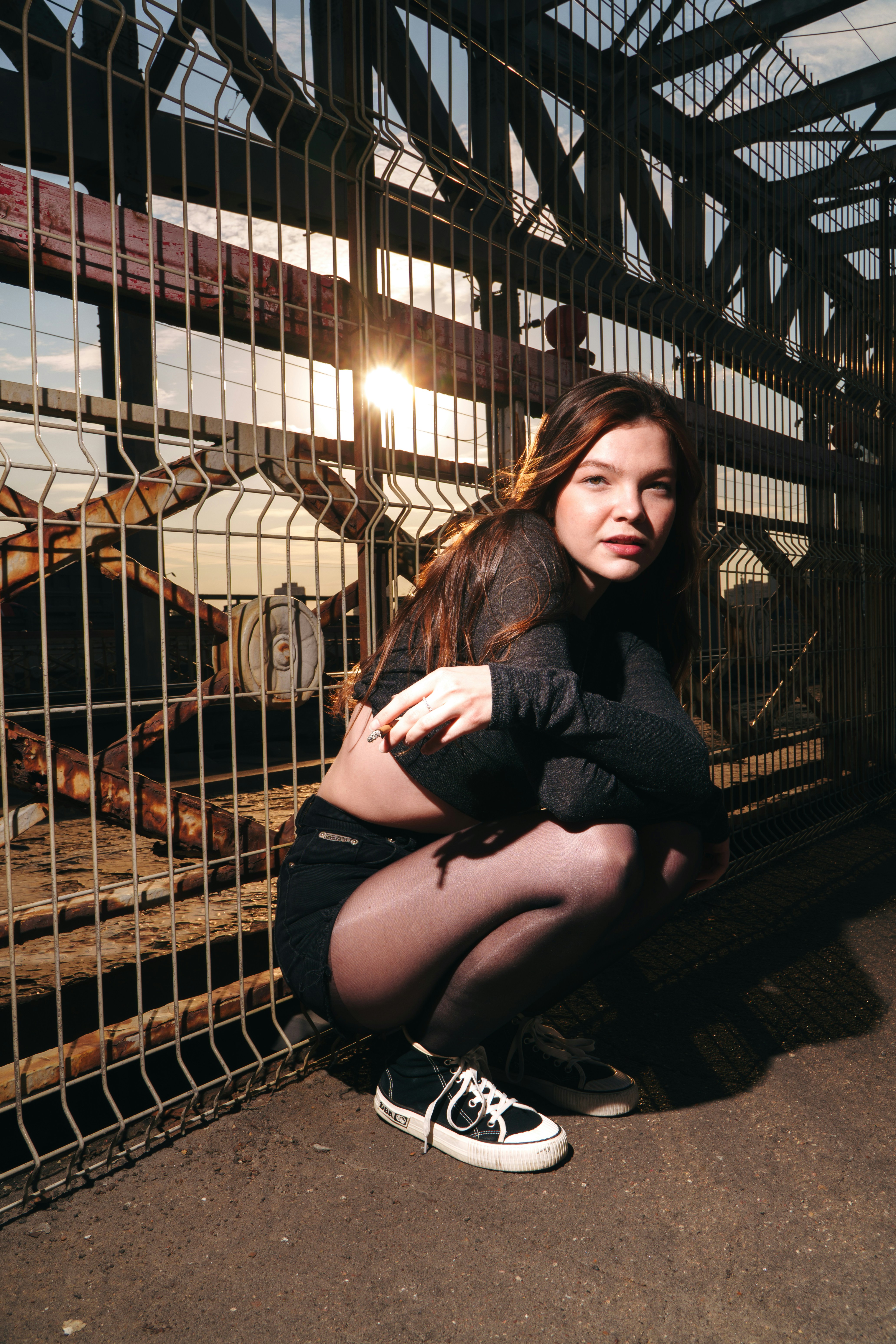 Crouched Confidence: Portrait by a Chain-Link Sunset