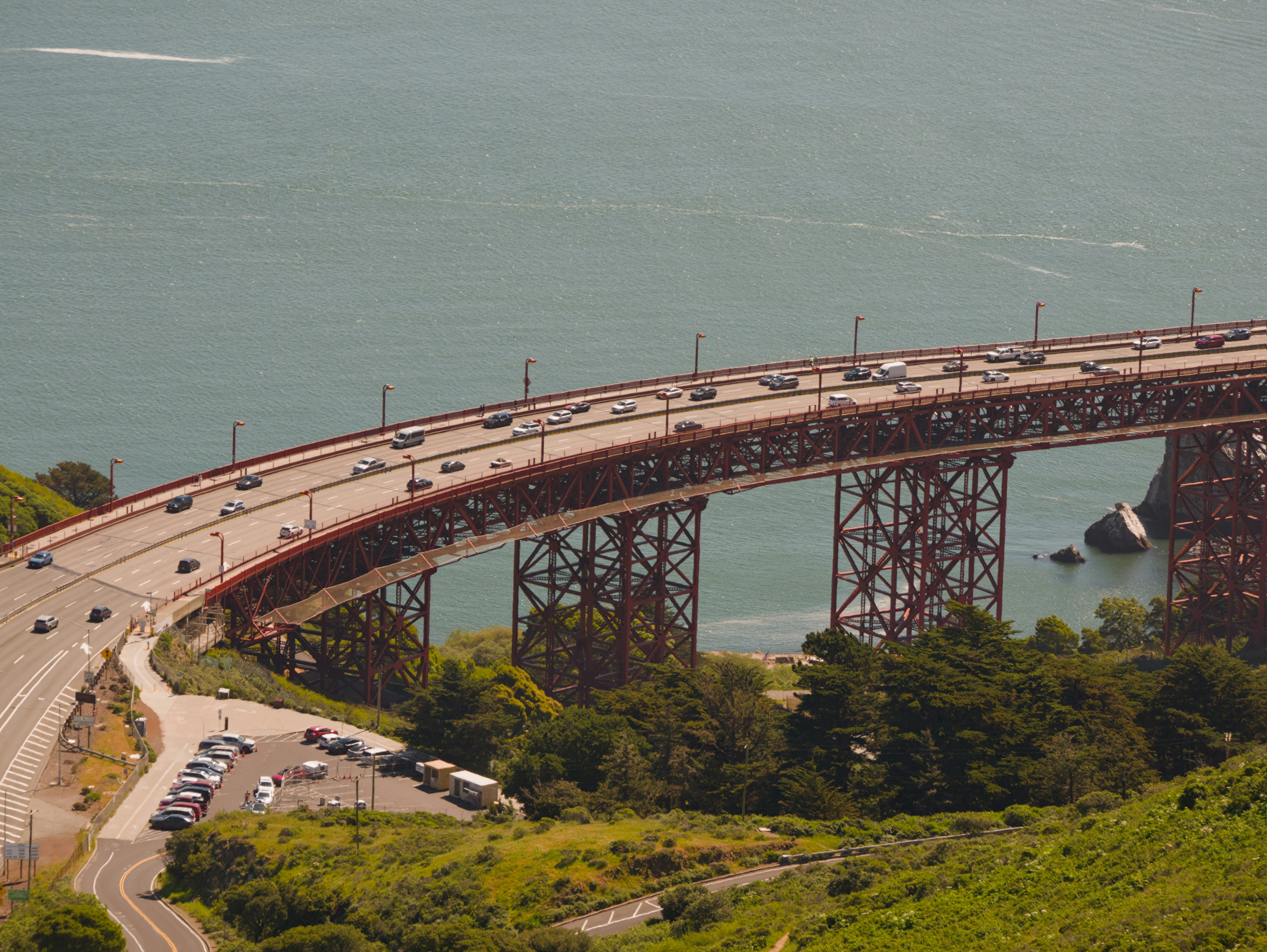 Curved Coastal Bridge Slice: Vehicles Cross a Red Iron Arc Above Green Hills