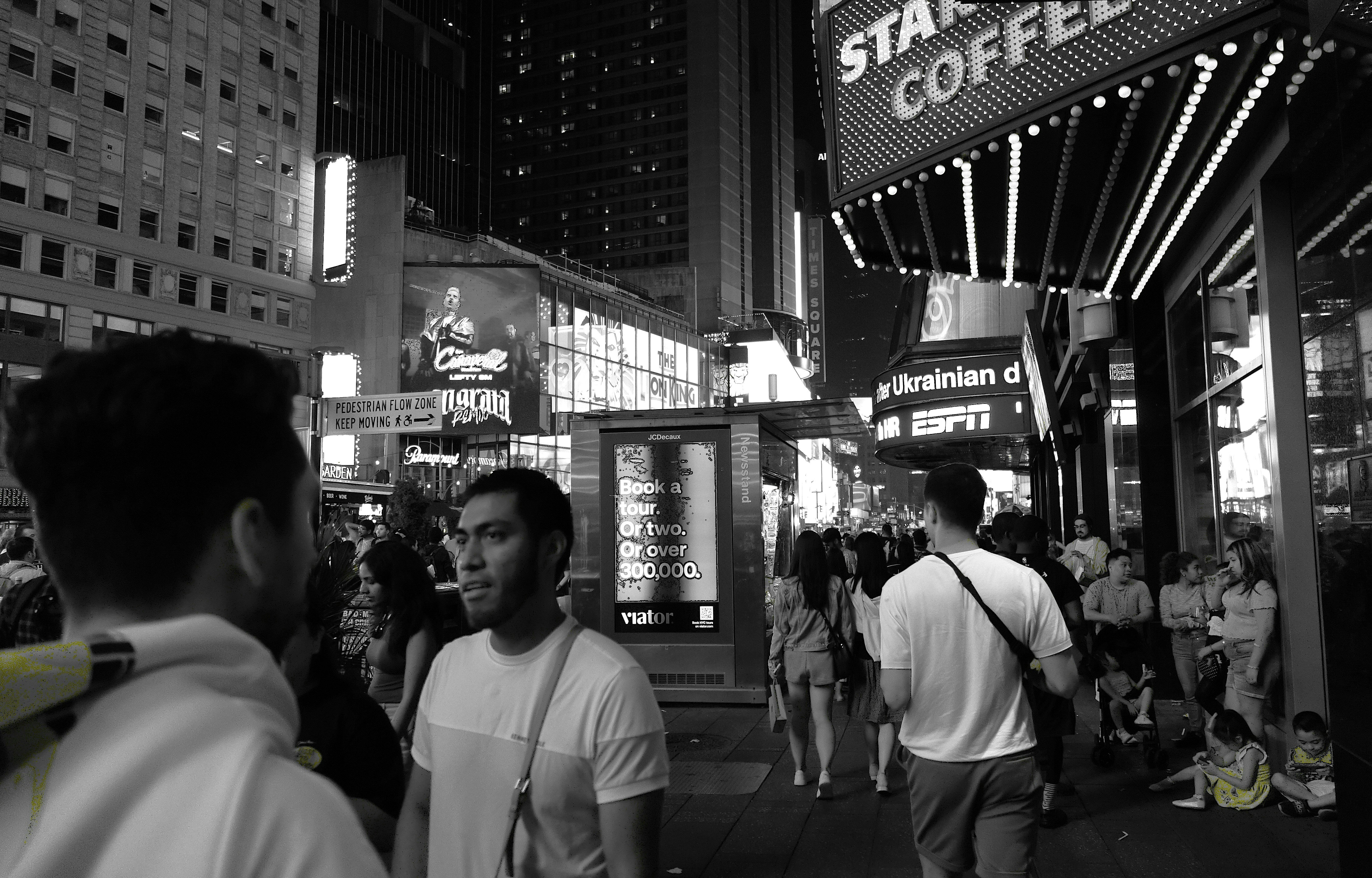 People walk past illuminated signs on a busy city street.