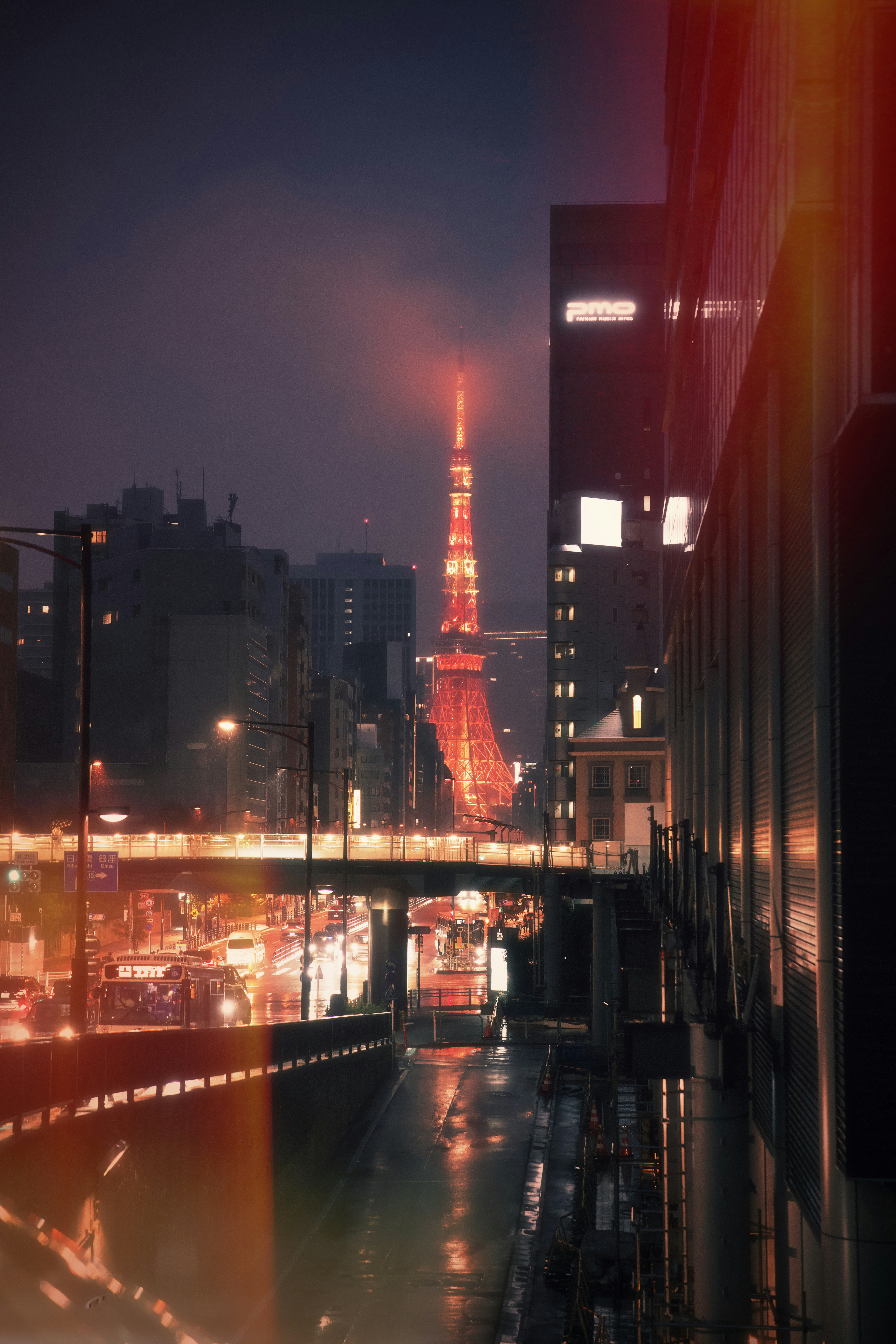 Tokyo Tower rises through urban glow above a rain-soaked street