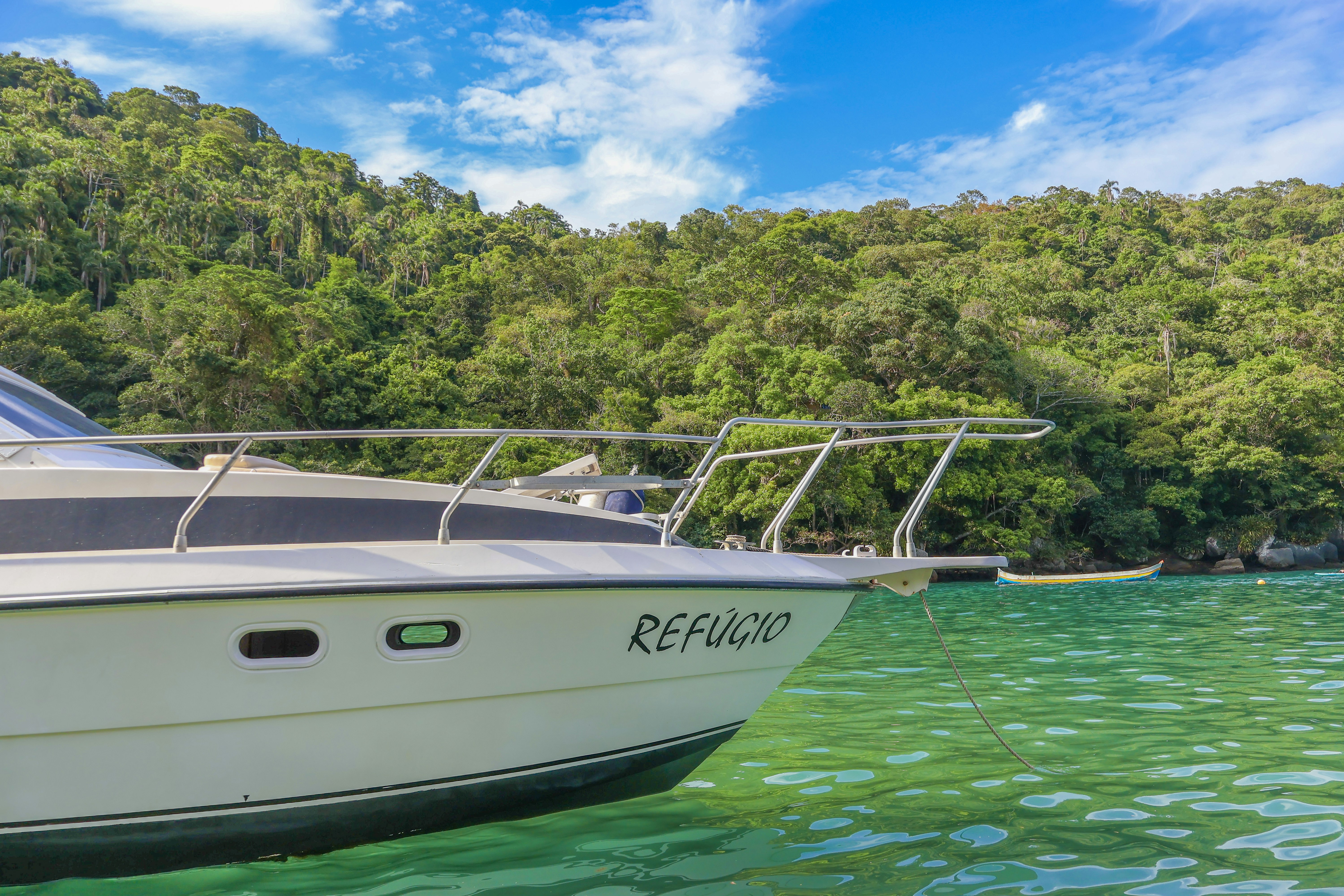 White boat named 'Refúgio' anchors along emerald lagoon surrounded by forest
