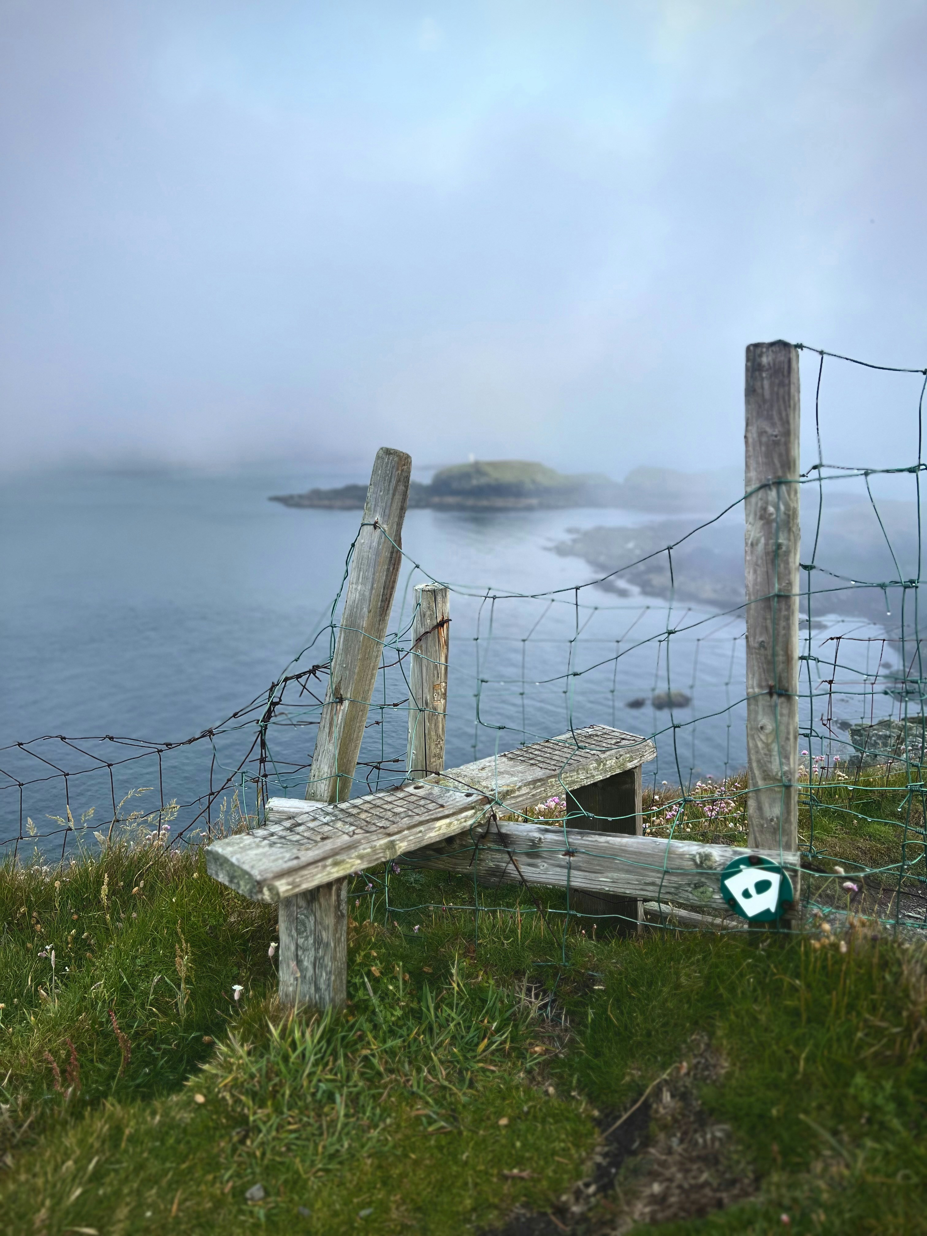Wooden stile and fence on a foggy coastal cliff.