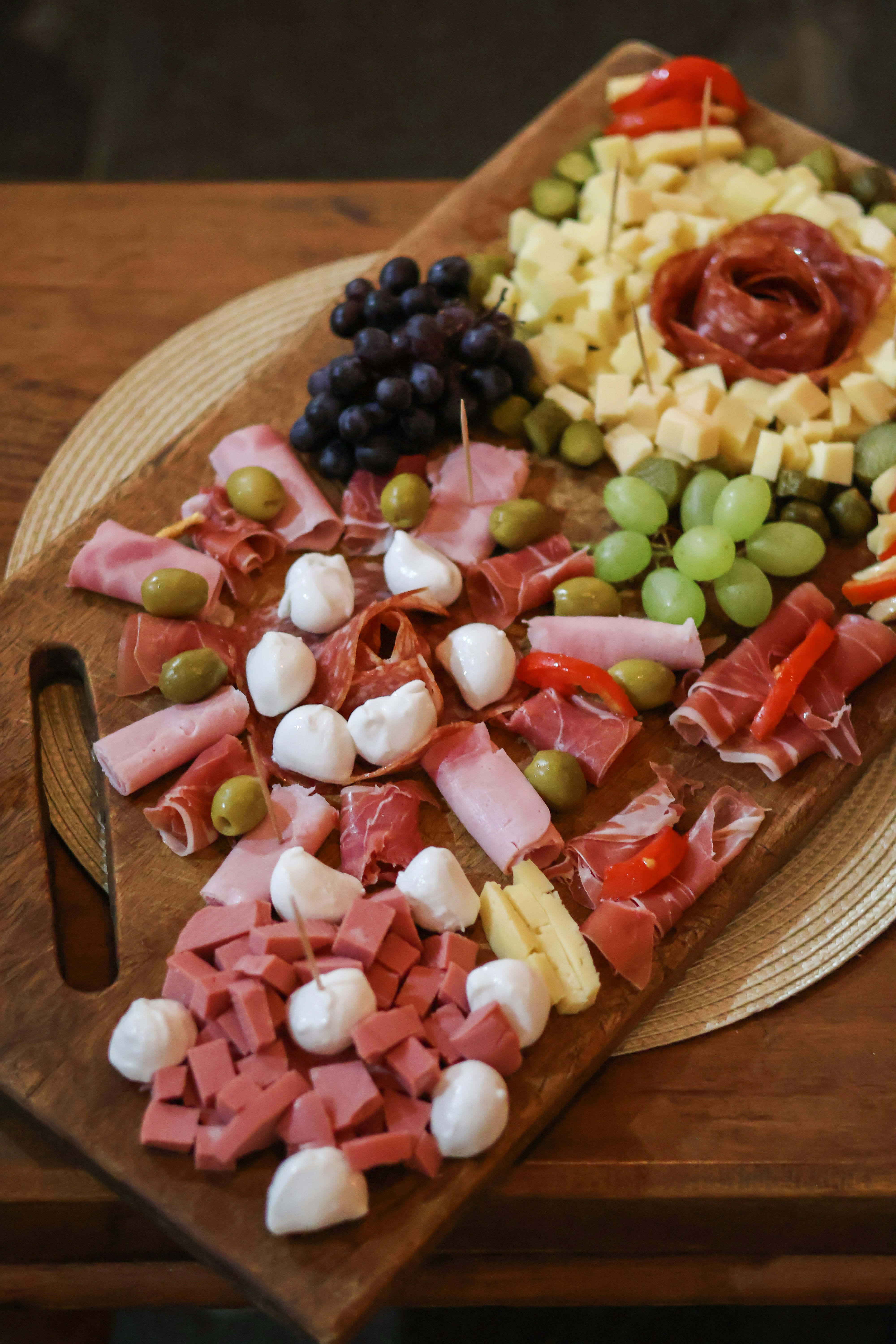 Close-up of an artisanal charcuterie board with cheeses, grapes, olives, mozzarella, and cured meats, beautifully arranged for a gourmet dining experience.