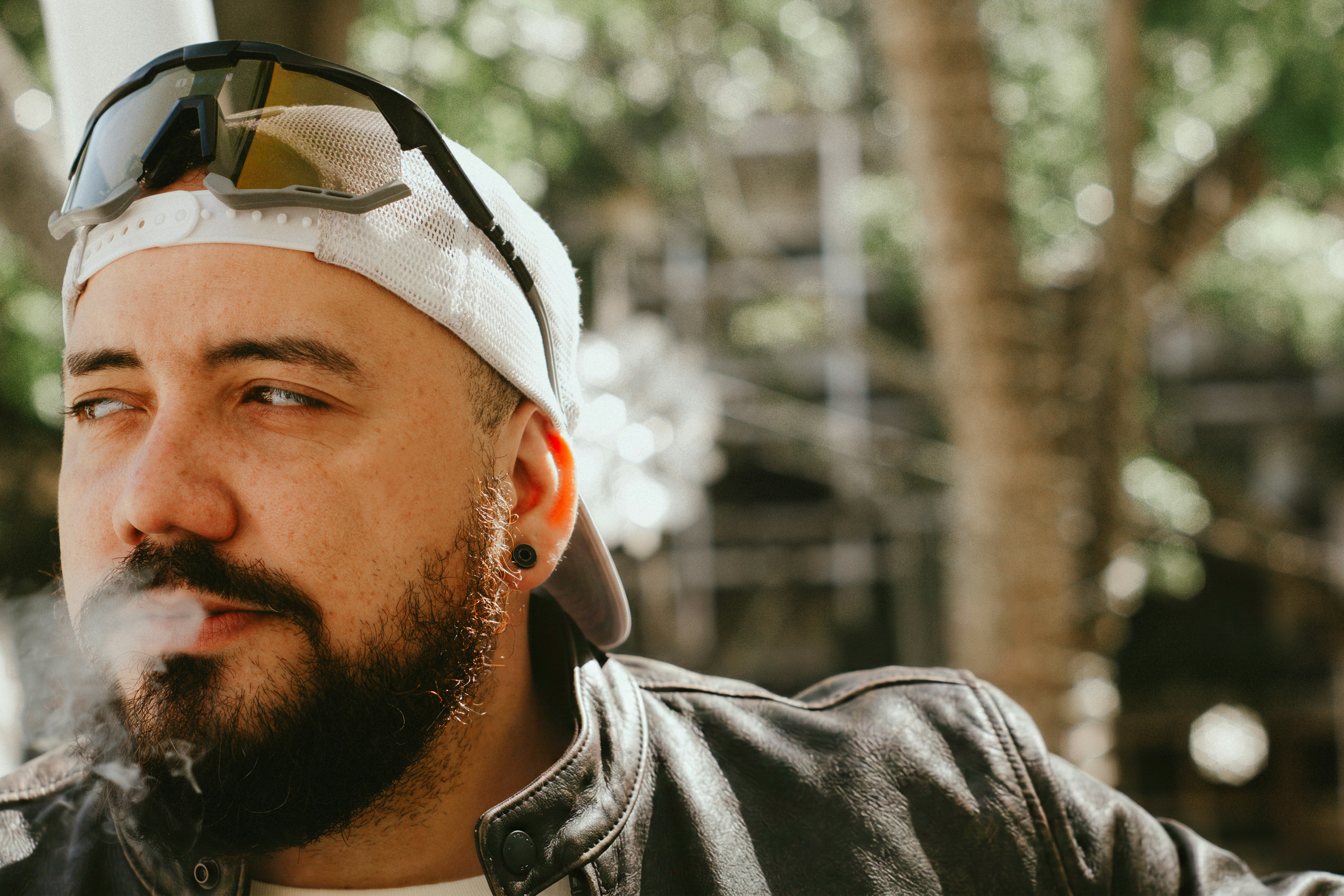 Hard-lidded gaze and smoke: a man with cap and beard in afternoon light