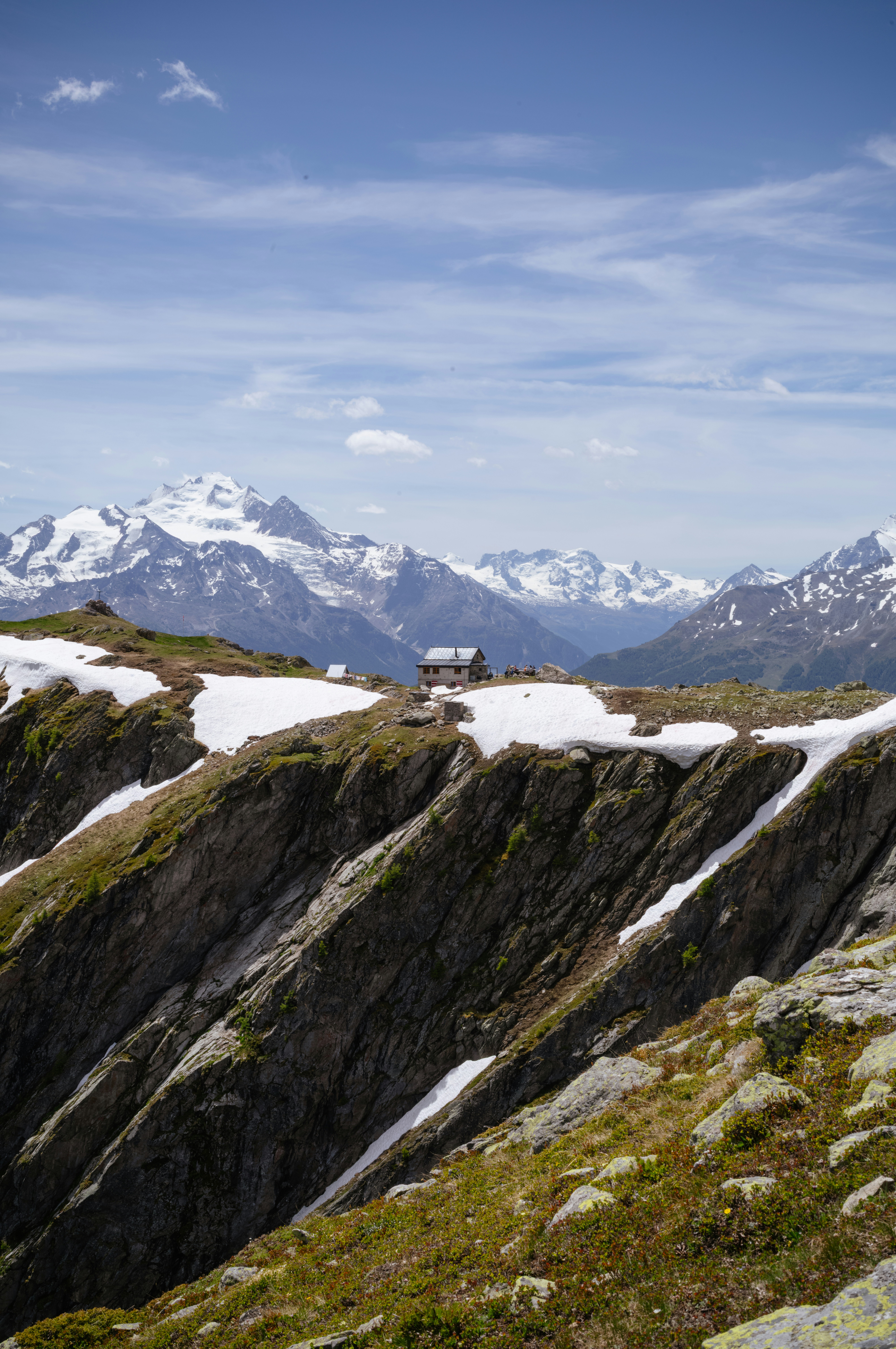Snow-dusted hut rests on a ridge as jagged peaks loom in the distance