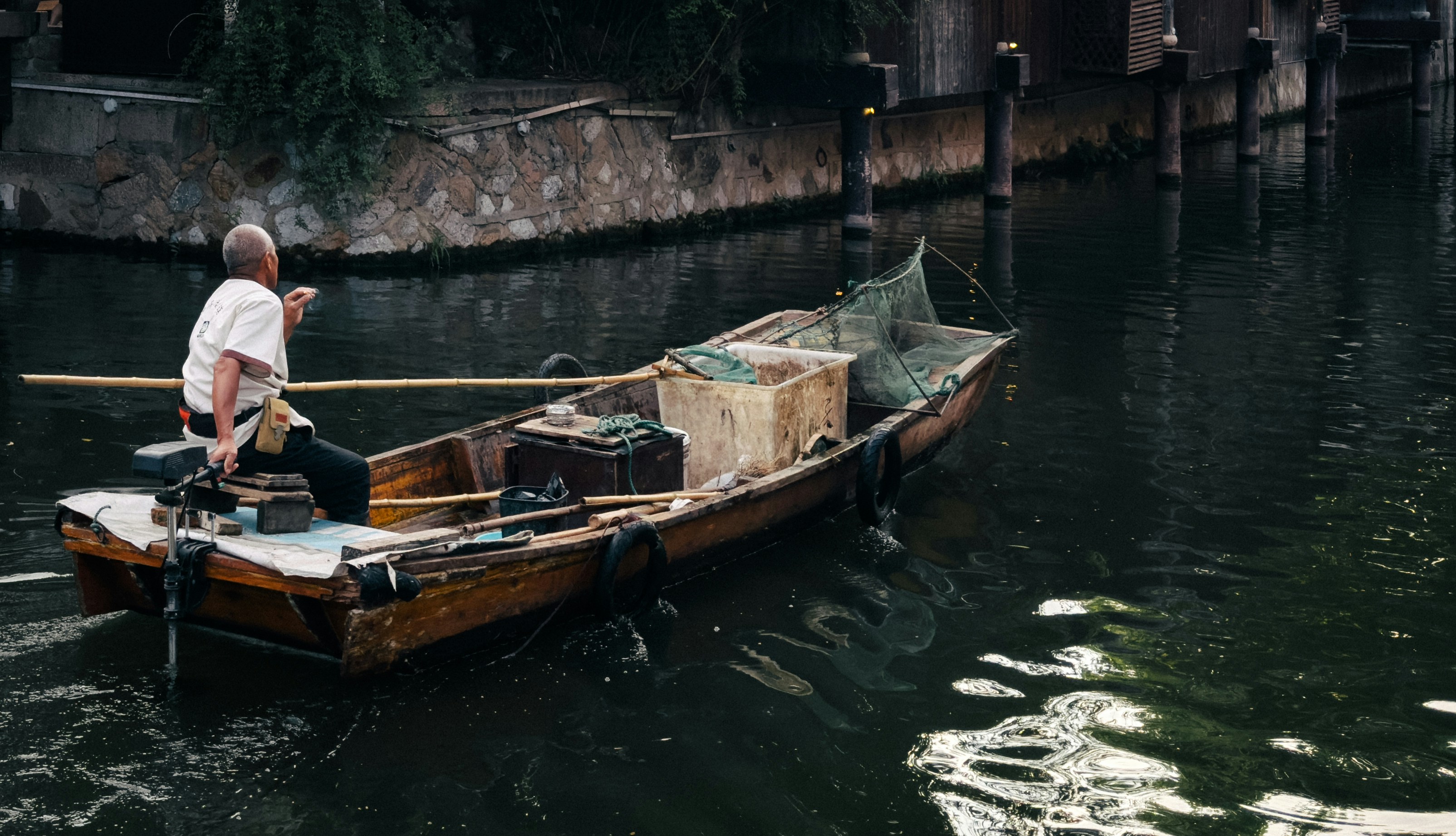 Older man navigates a wooden boat on a calm canal.