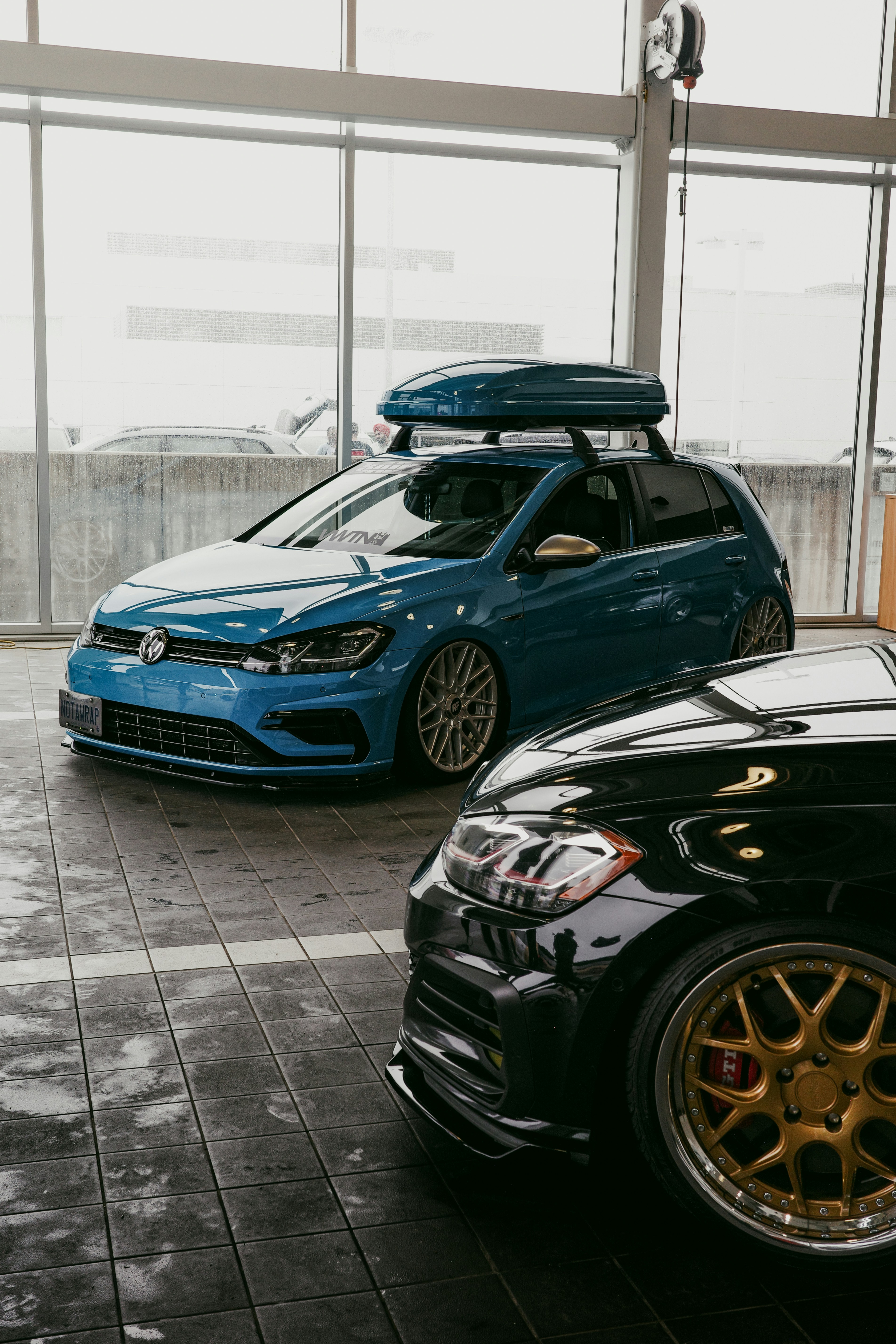 Modified blue volkswagen golf with roof box and black car.