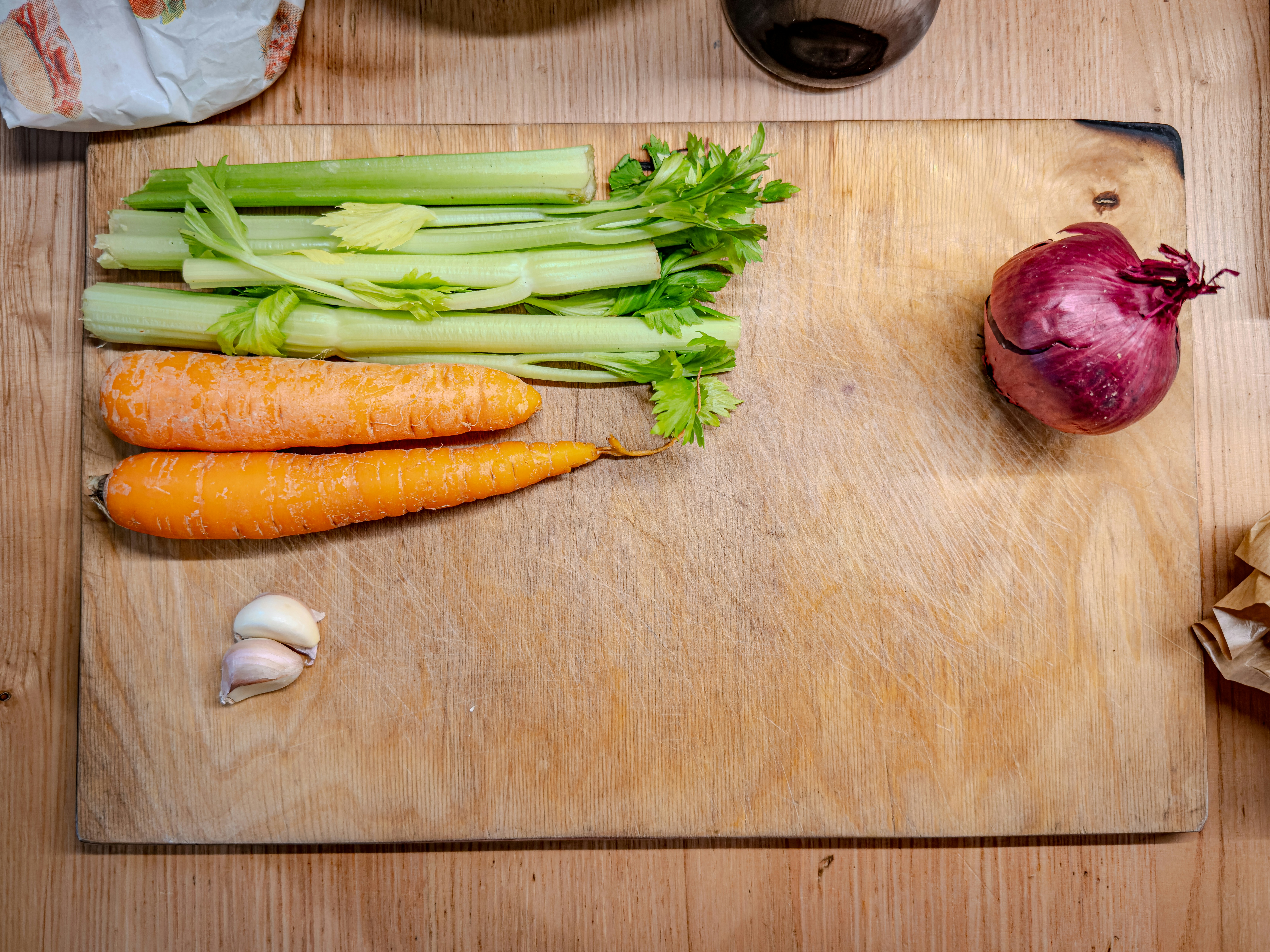 Celery, carrots, an onion and garlic cloves, waiting to be chopped, on a well-used chopping board on a kitchen work surface