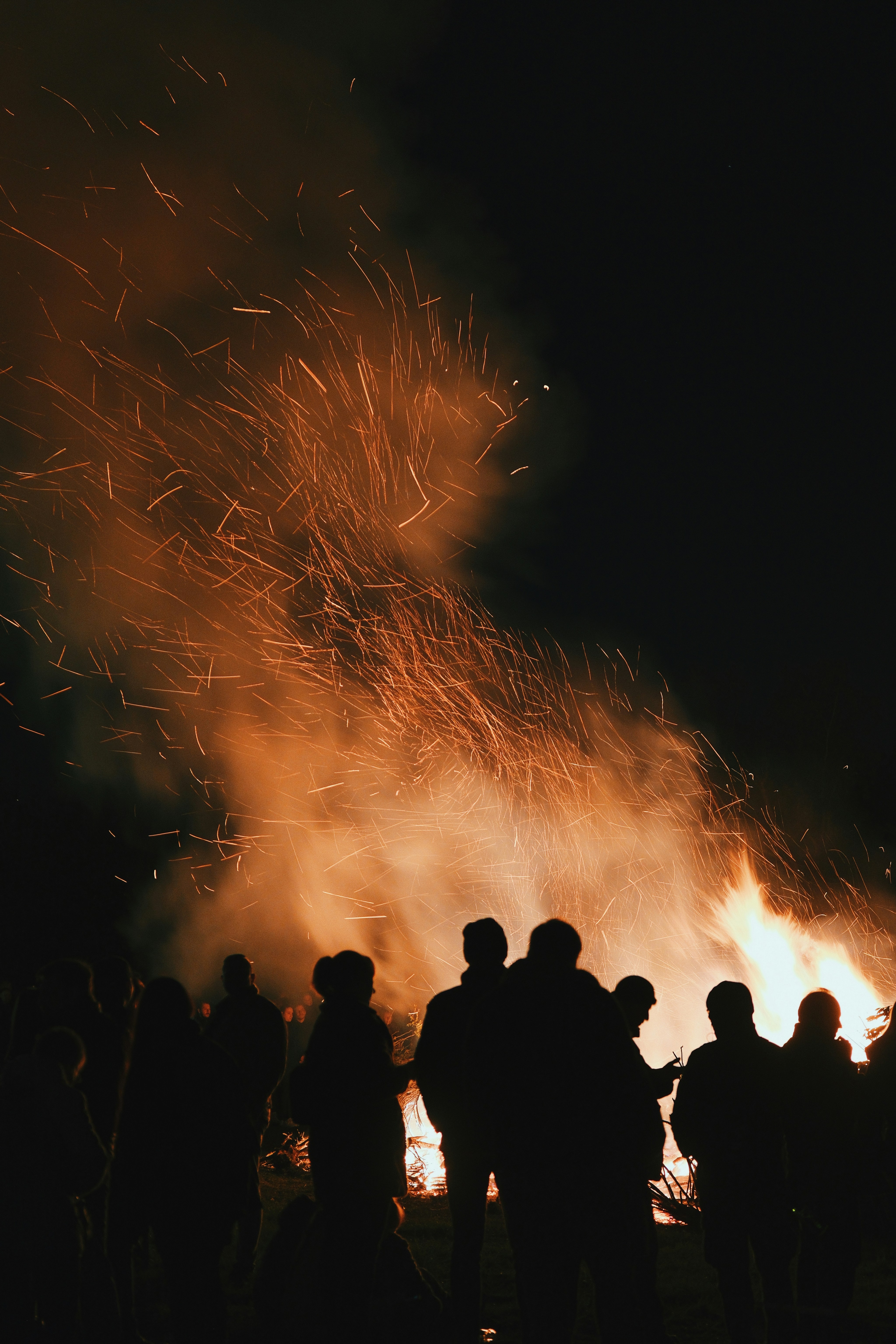 Silhouettes of people gathered around a large bonfire at night.