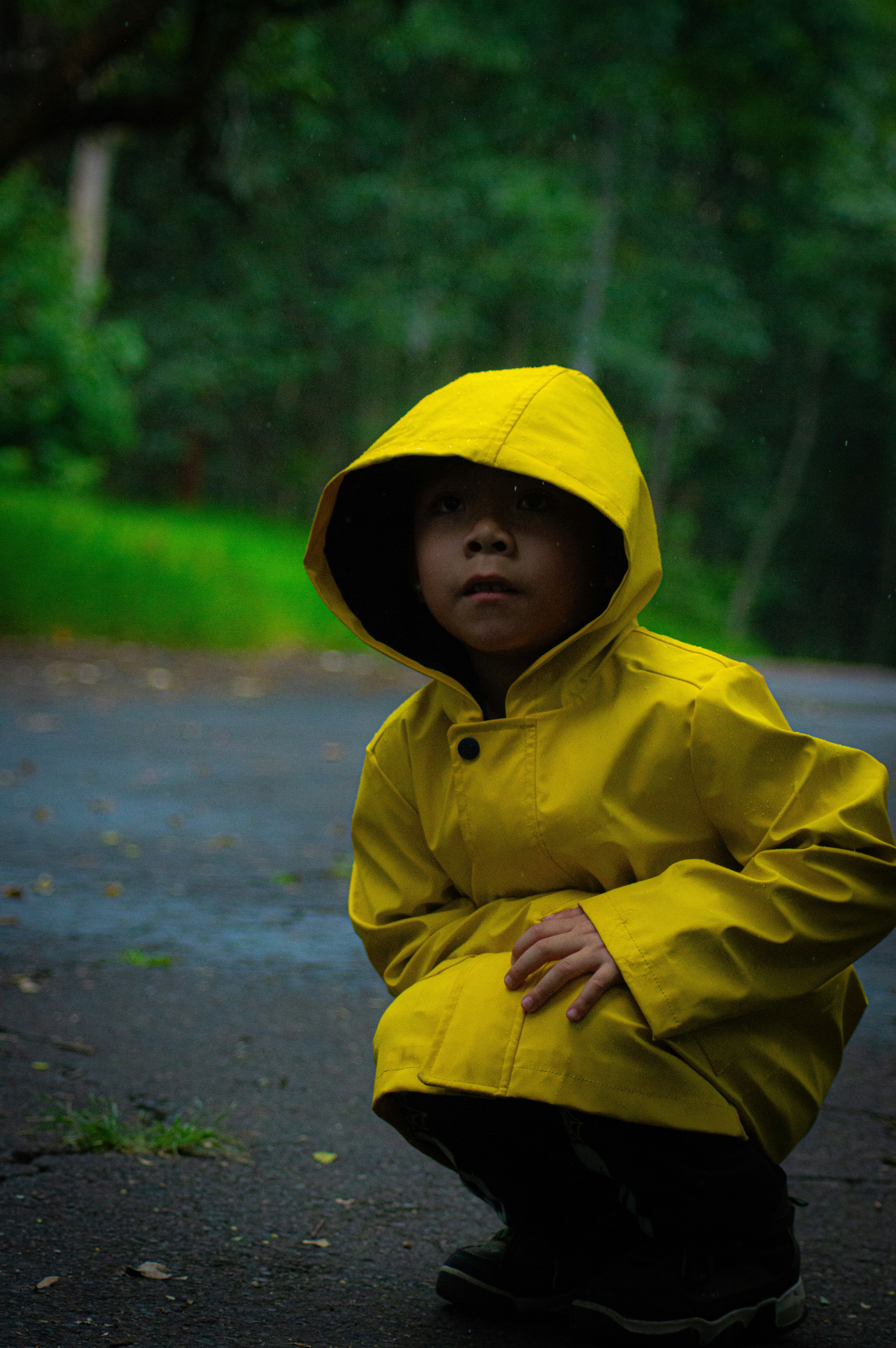Yellow Raincoat Wonder: A Child Squats in the Wet Park