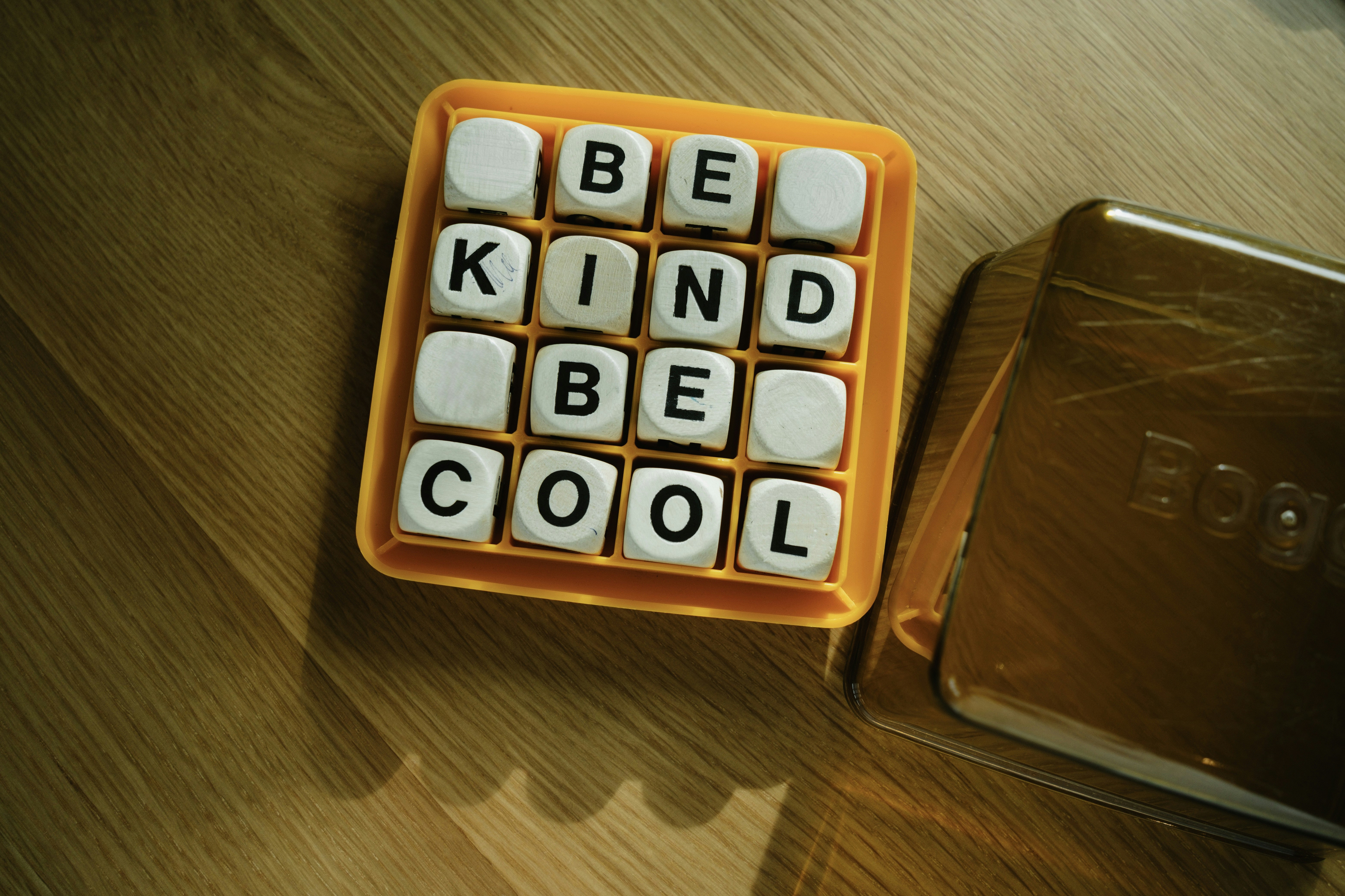 White letter dice spelling 'be kind be cool' on wood.