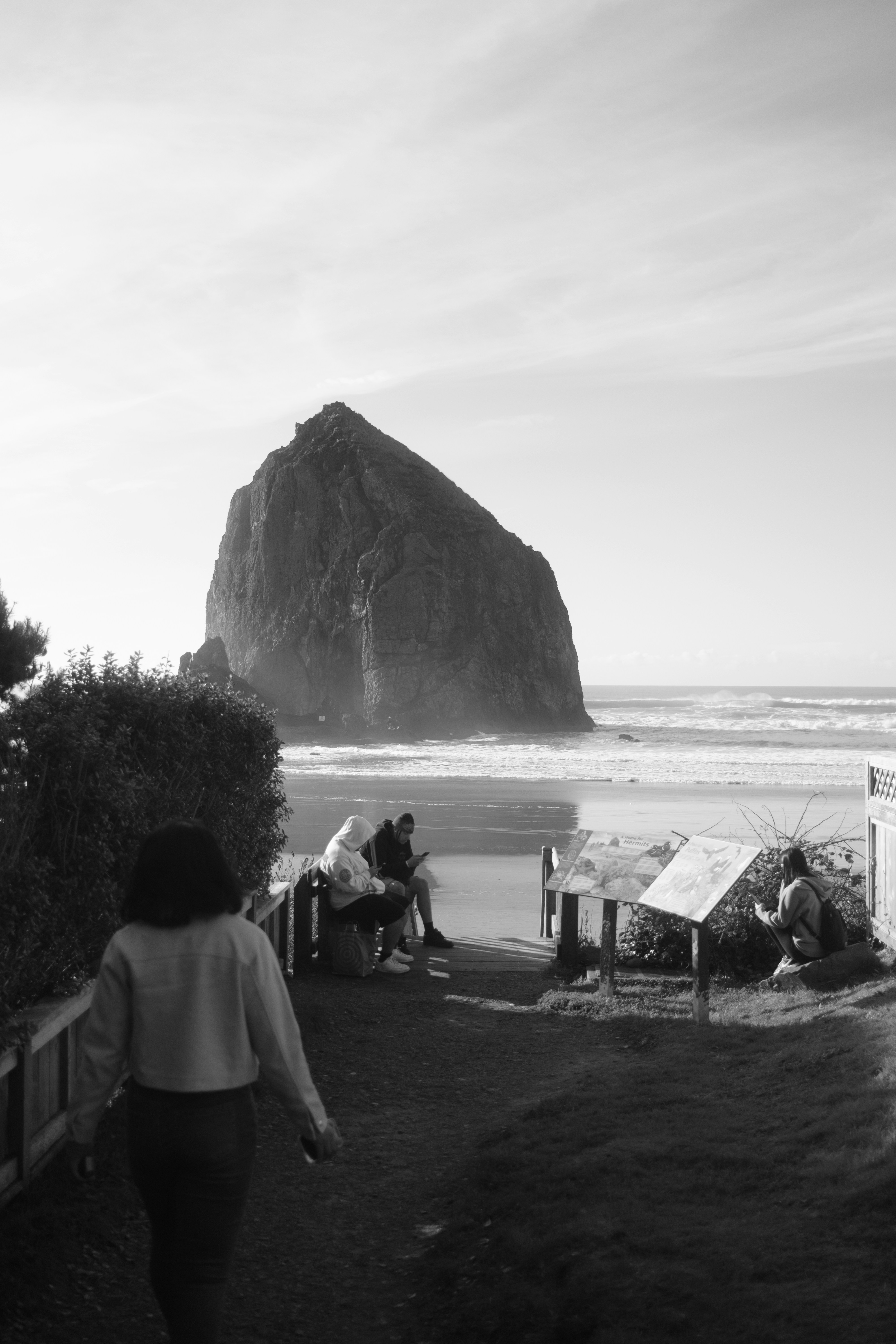 Woman walks towards haystack rock and people on the beach.