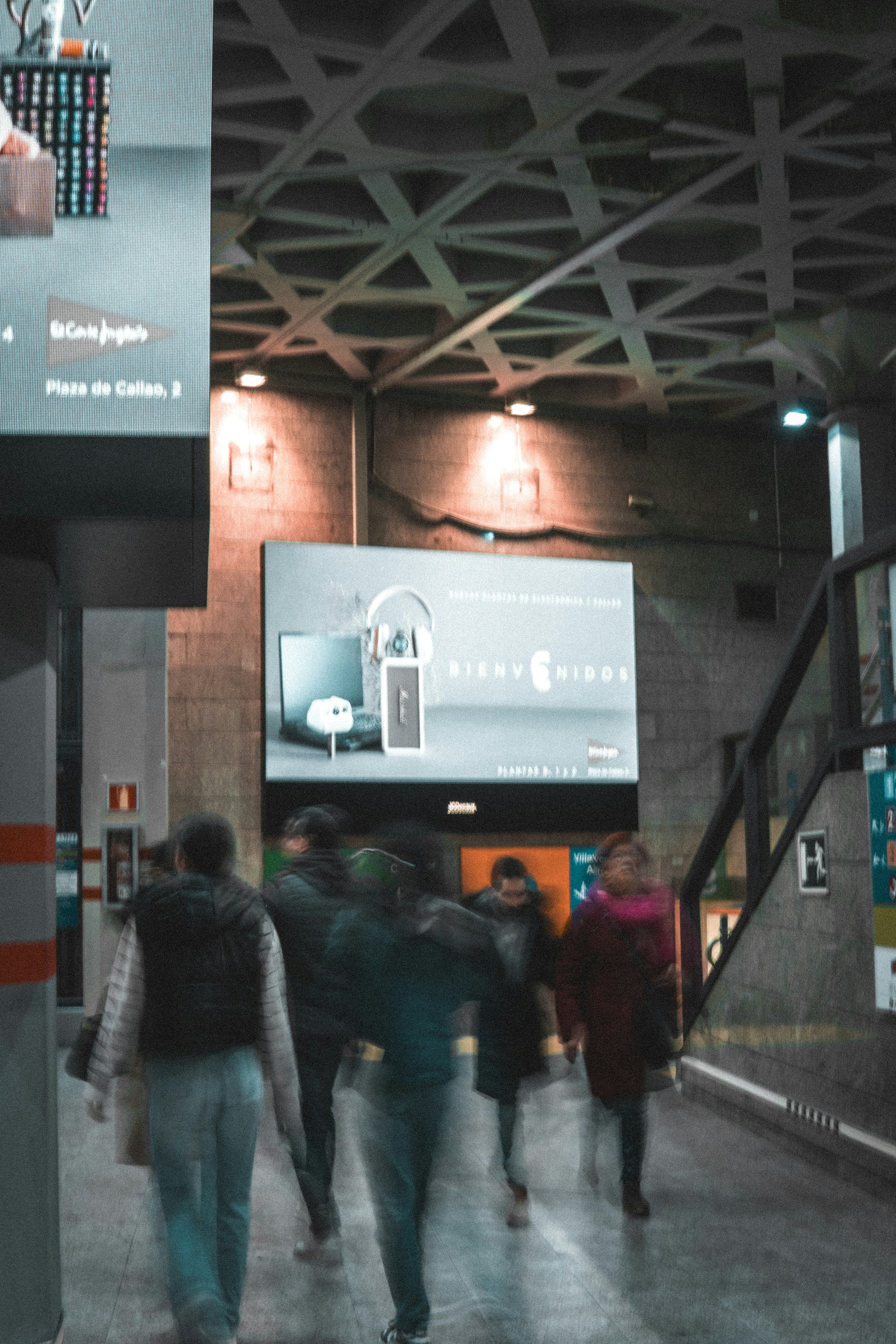 People in Transit Beneath a Geometric Ceiling Advertisement