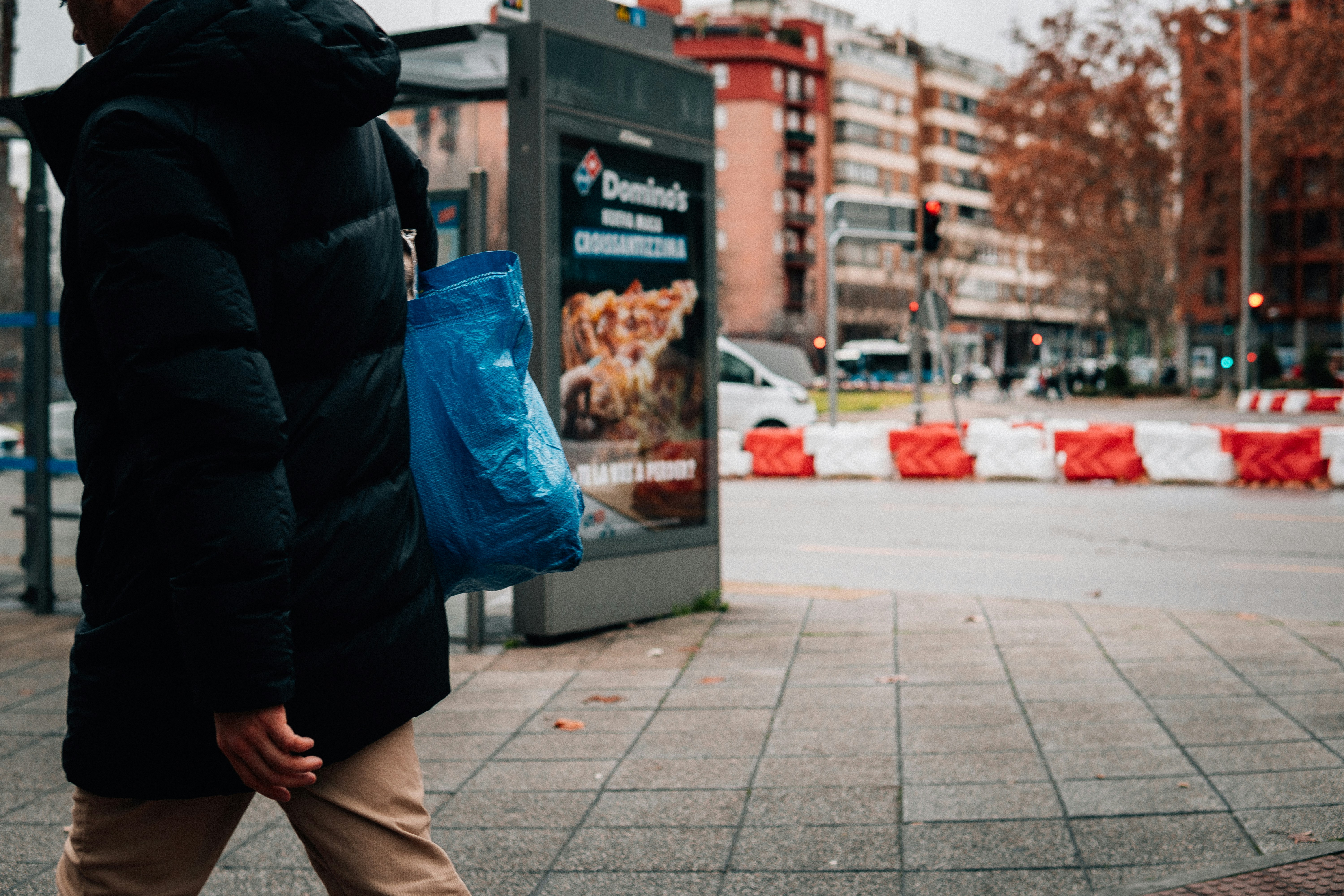 Masked stride: a passerby with a blue tote walks past a city bus stop