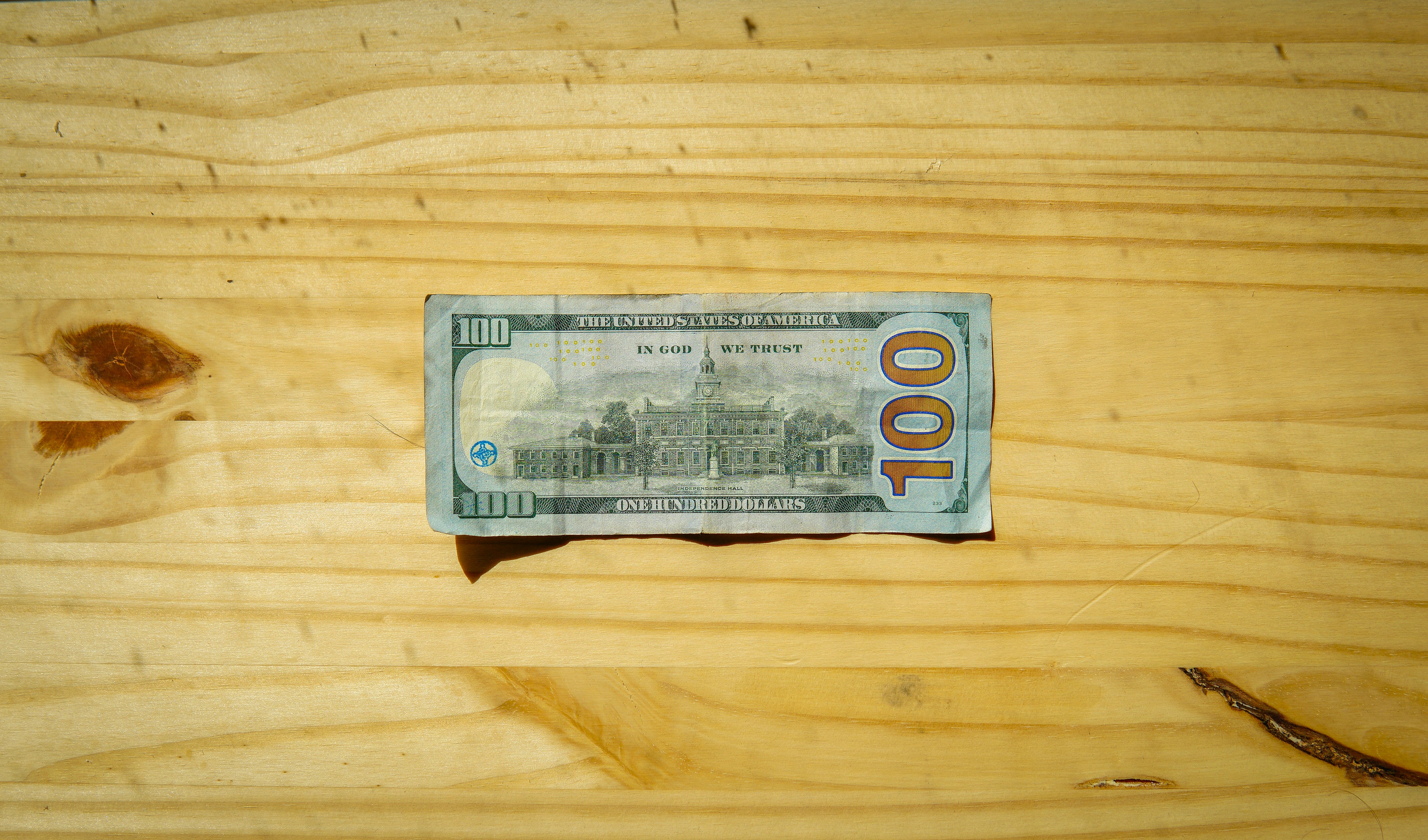 Folded hundred on sunlit pine tabletop