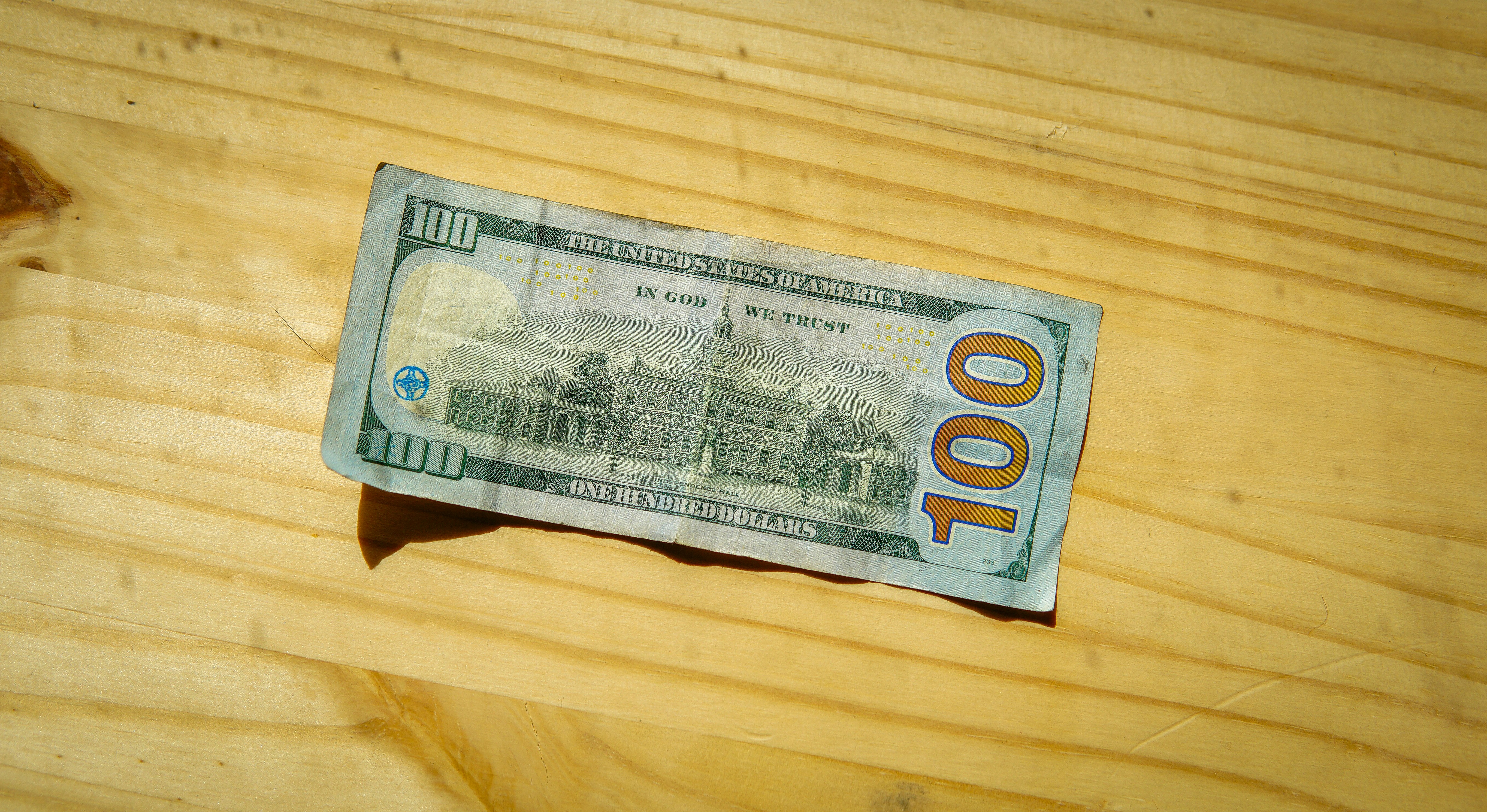 Folded hundred: a single $100 bill peeks from a wooden grain