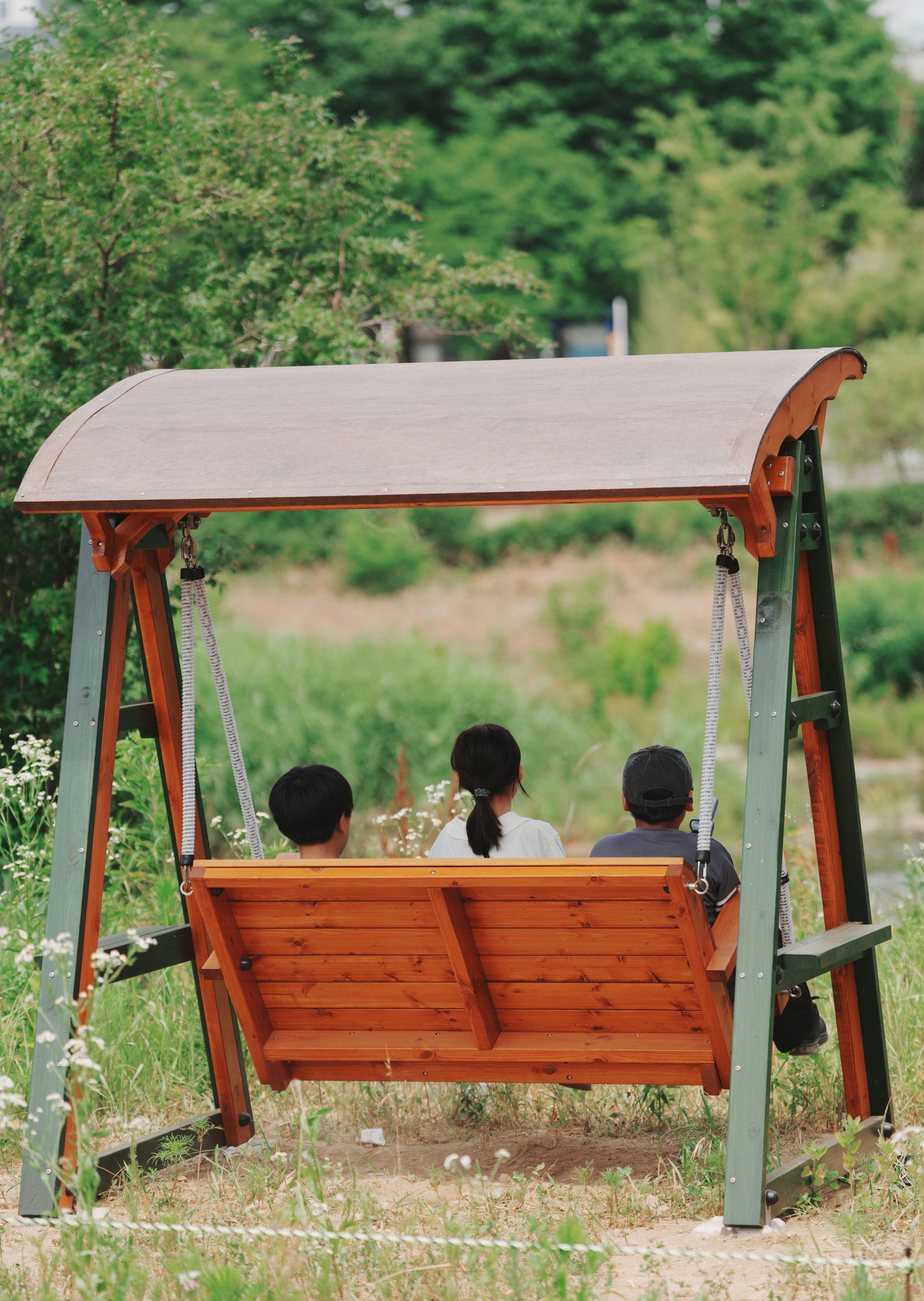 Three silhouettes on a wooden garden swing facing a sunlit meadow