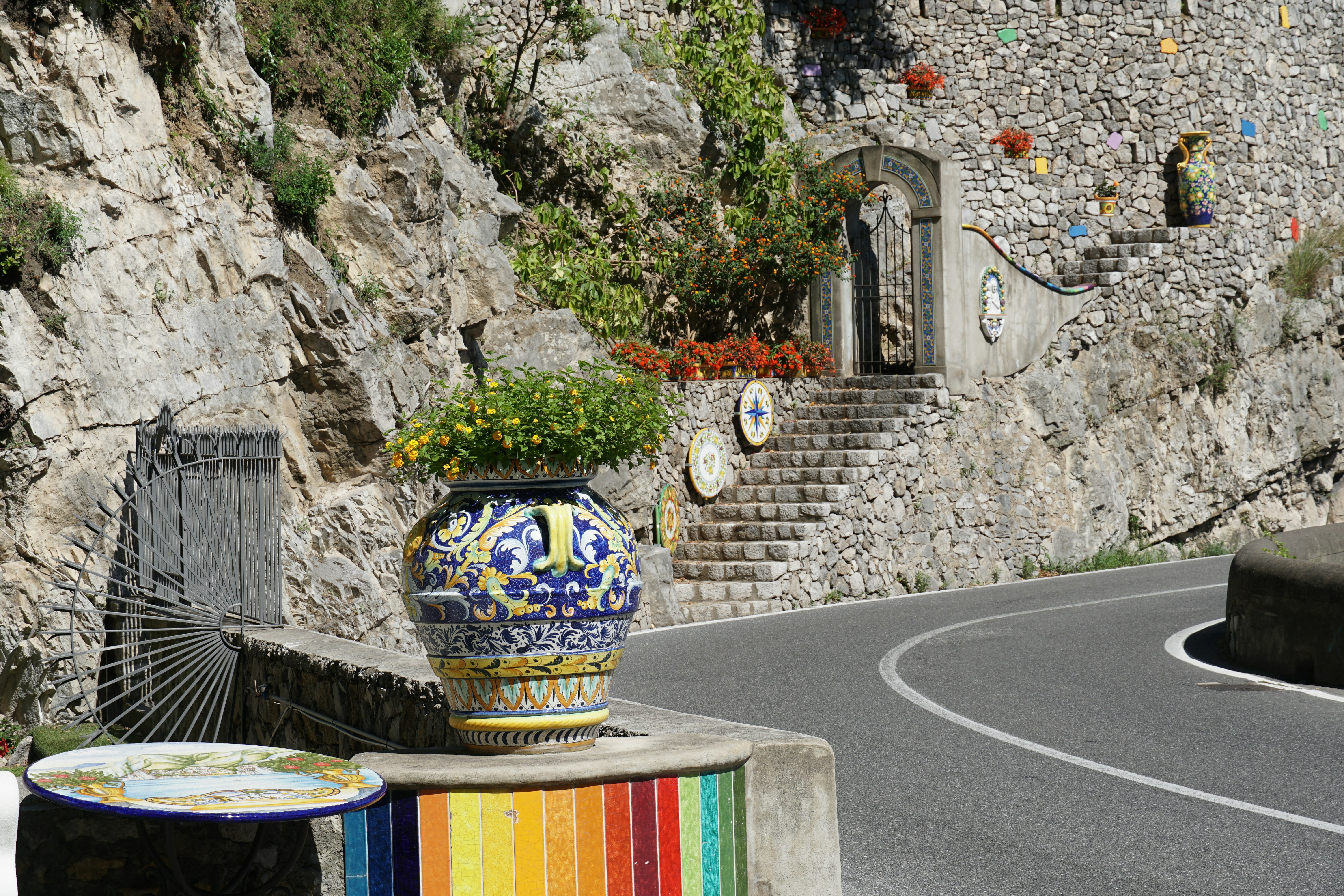 Colorful overlook: ceramic vase and rainbow pedestal by a winding Italian hillside road