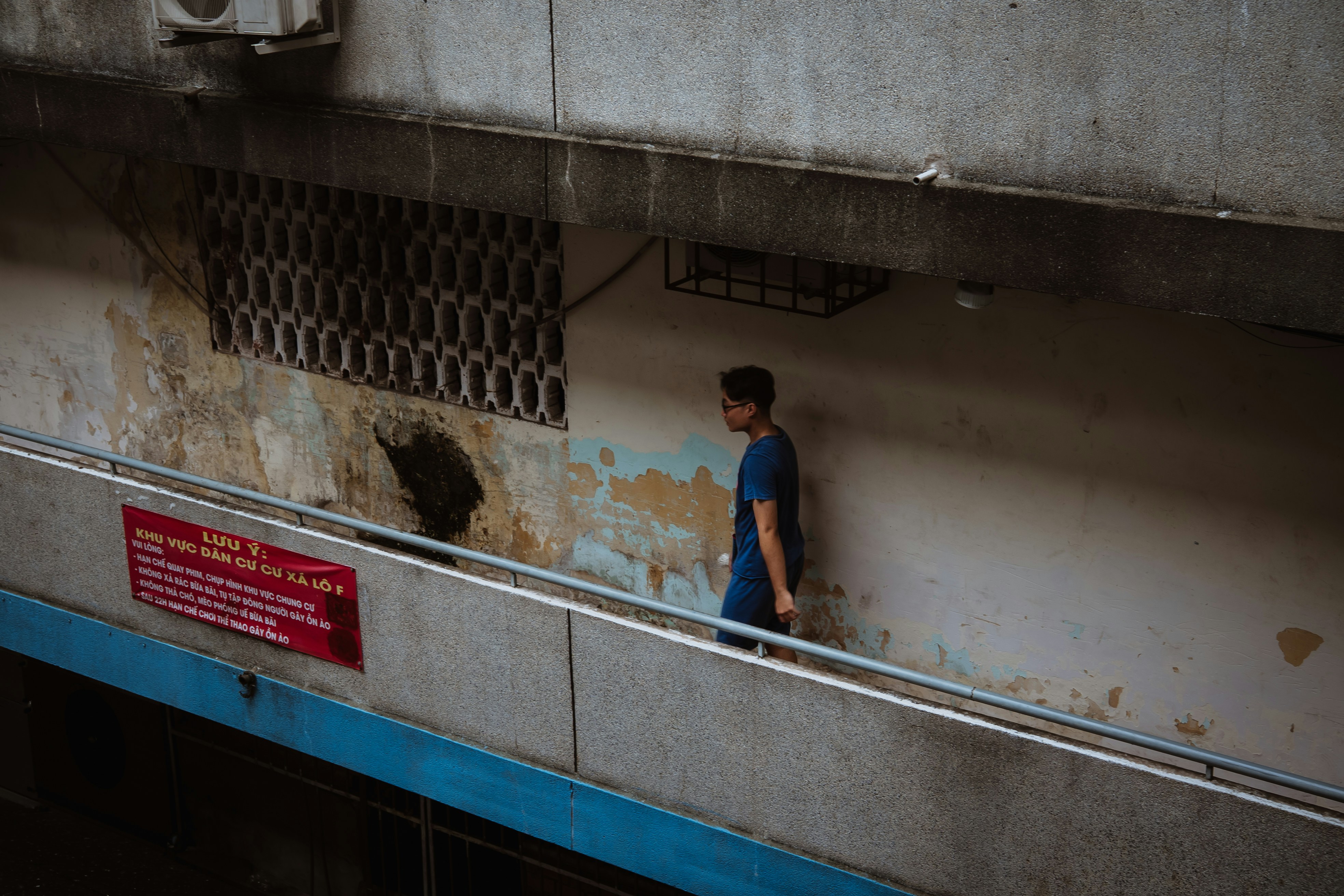 Man in a blue shirt walking along a weathered concrete corridor