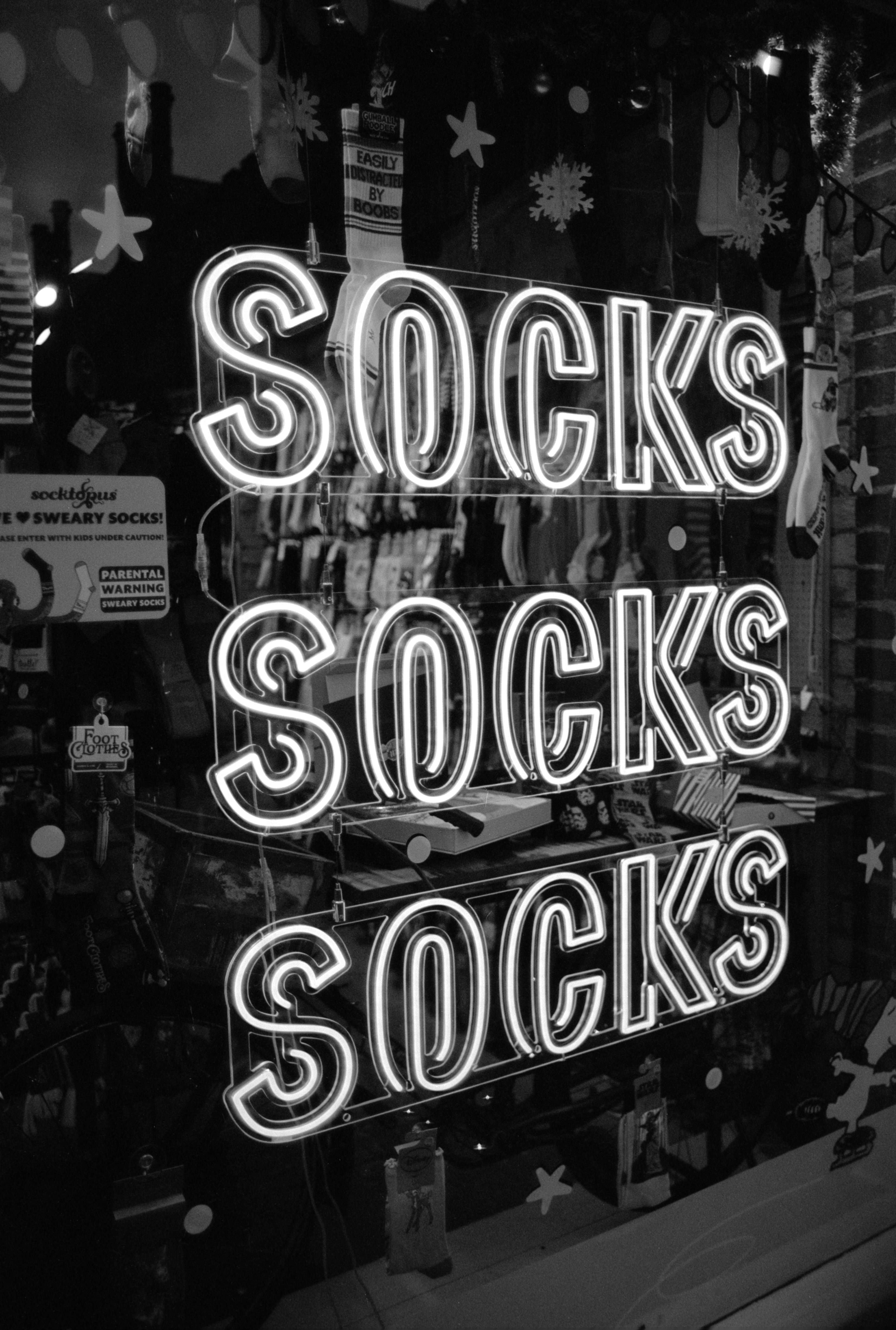 A neon sign repeats the word socks three times in a playful, cluttered shop window.
