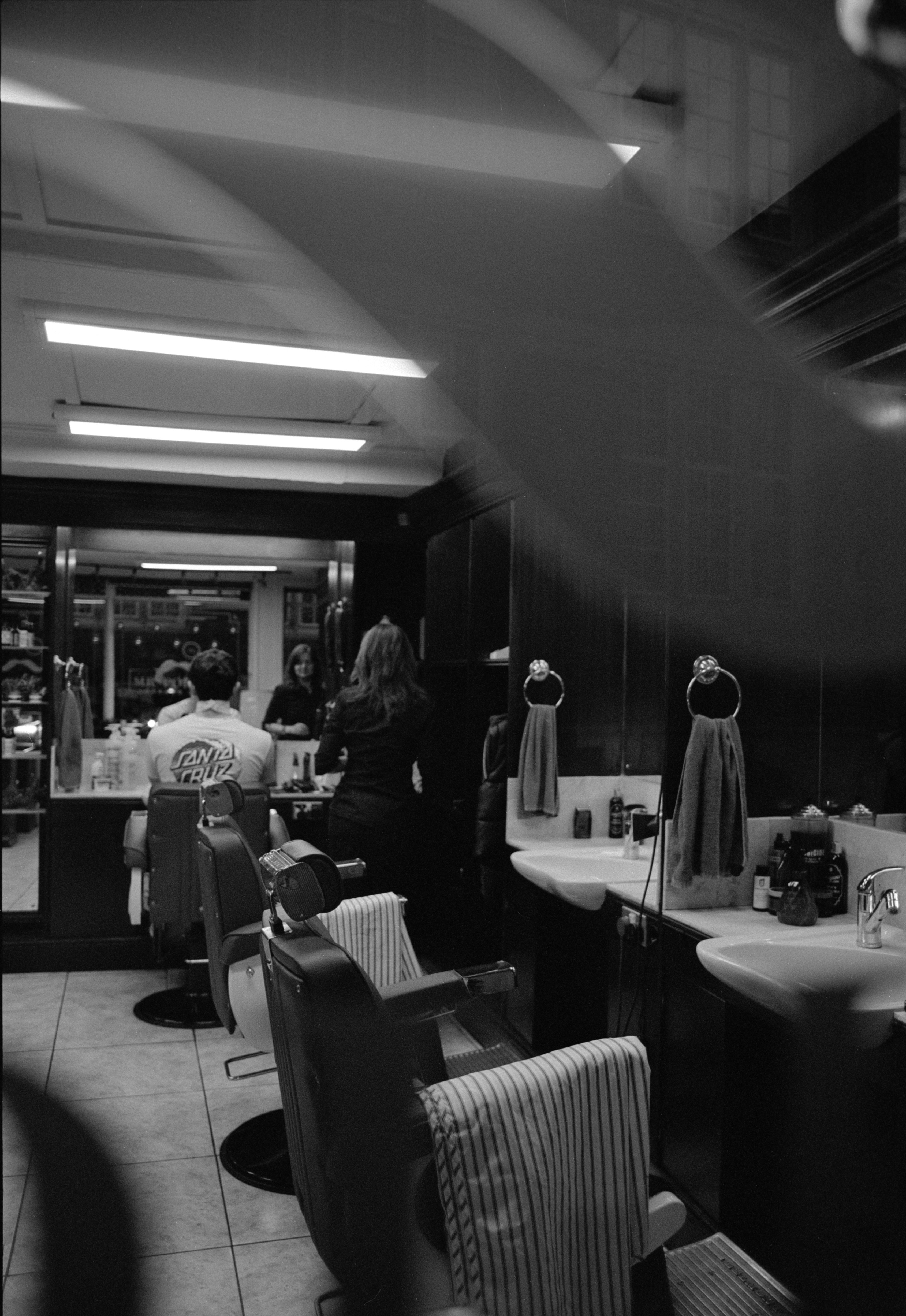 Vintage barber chairs and mirrors fill a quiet traditional barbershop in the evening light.