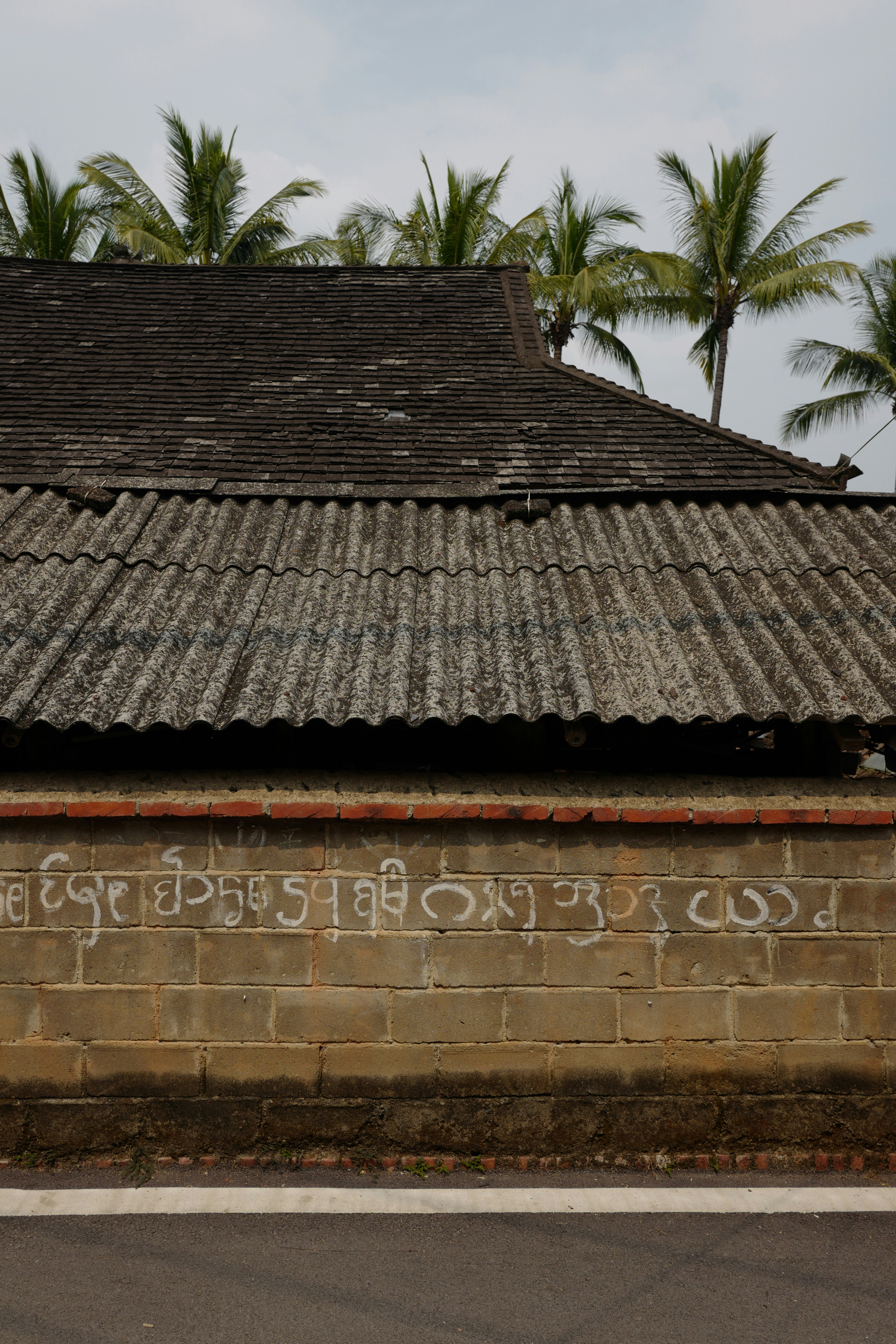 Stone wall with script, corrugated roof, and palm trees.