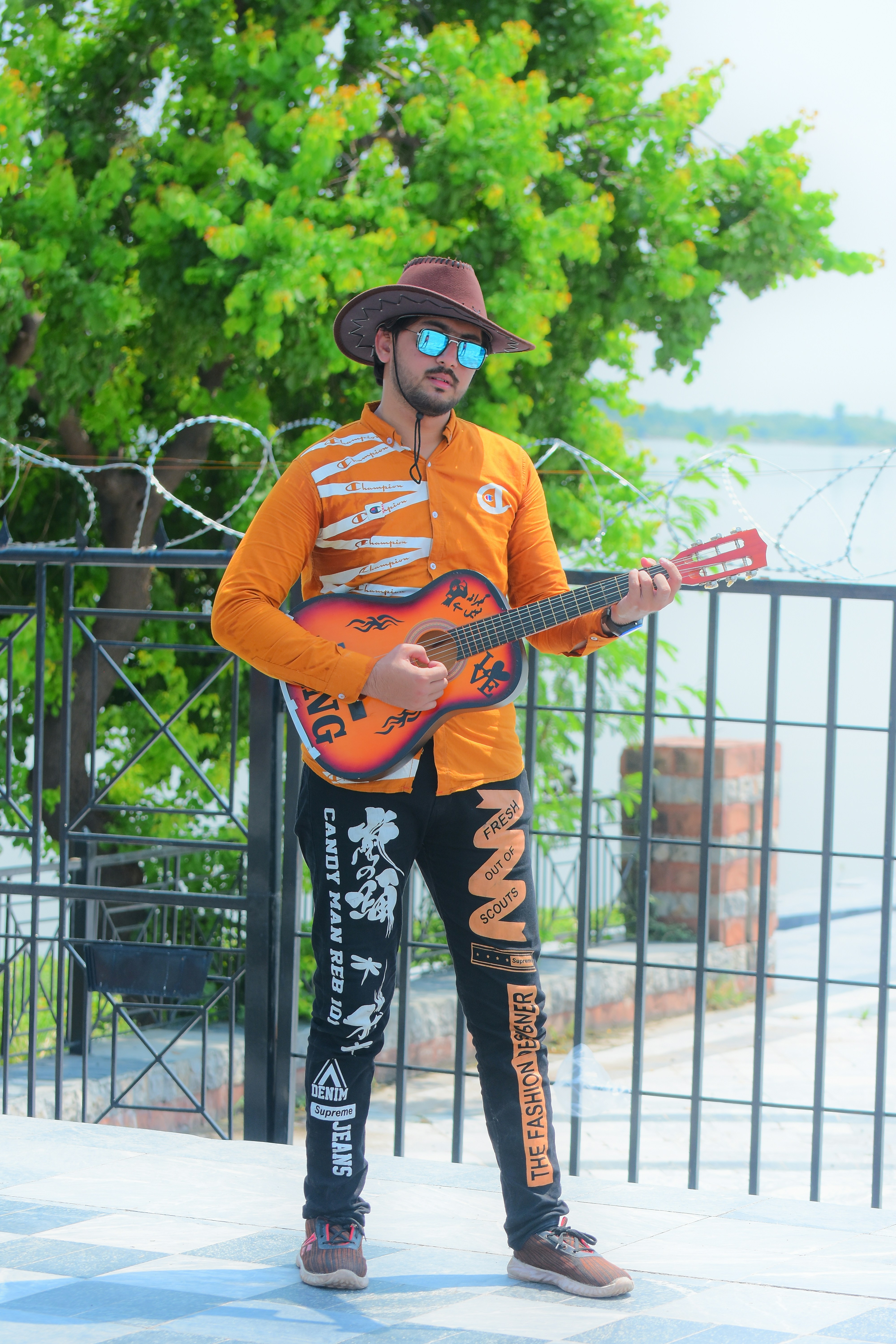 Orange-clad Street Musician Strums a Sunny Guitara on a Waterfront Promenade