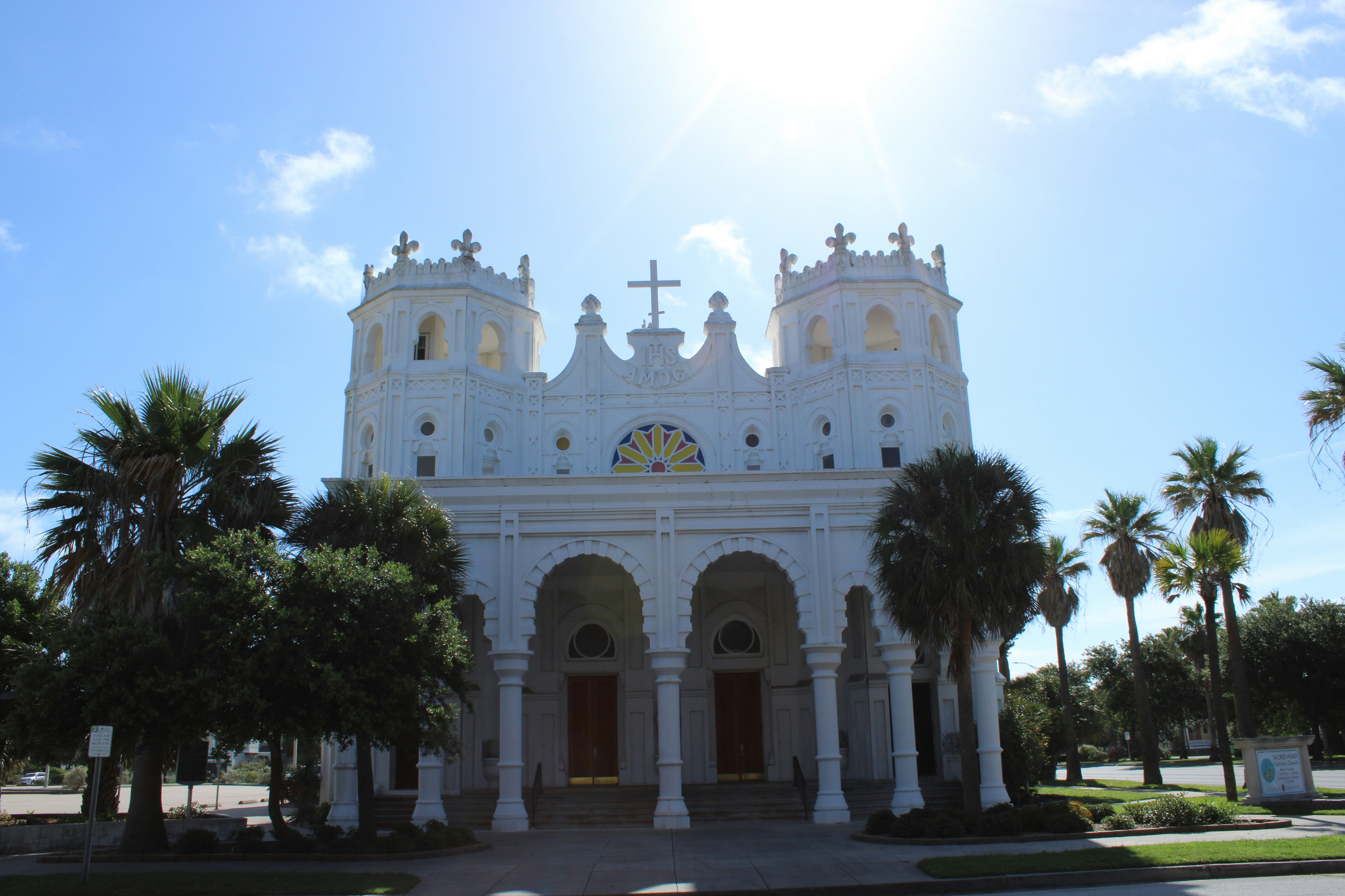 Sunlit white church with palm-lined approach under a bright midday sky