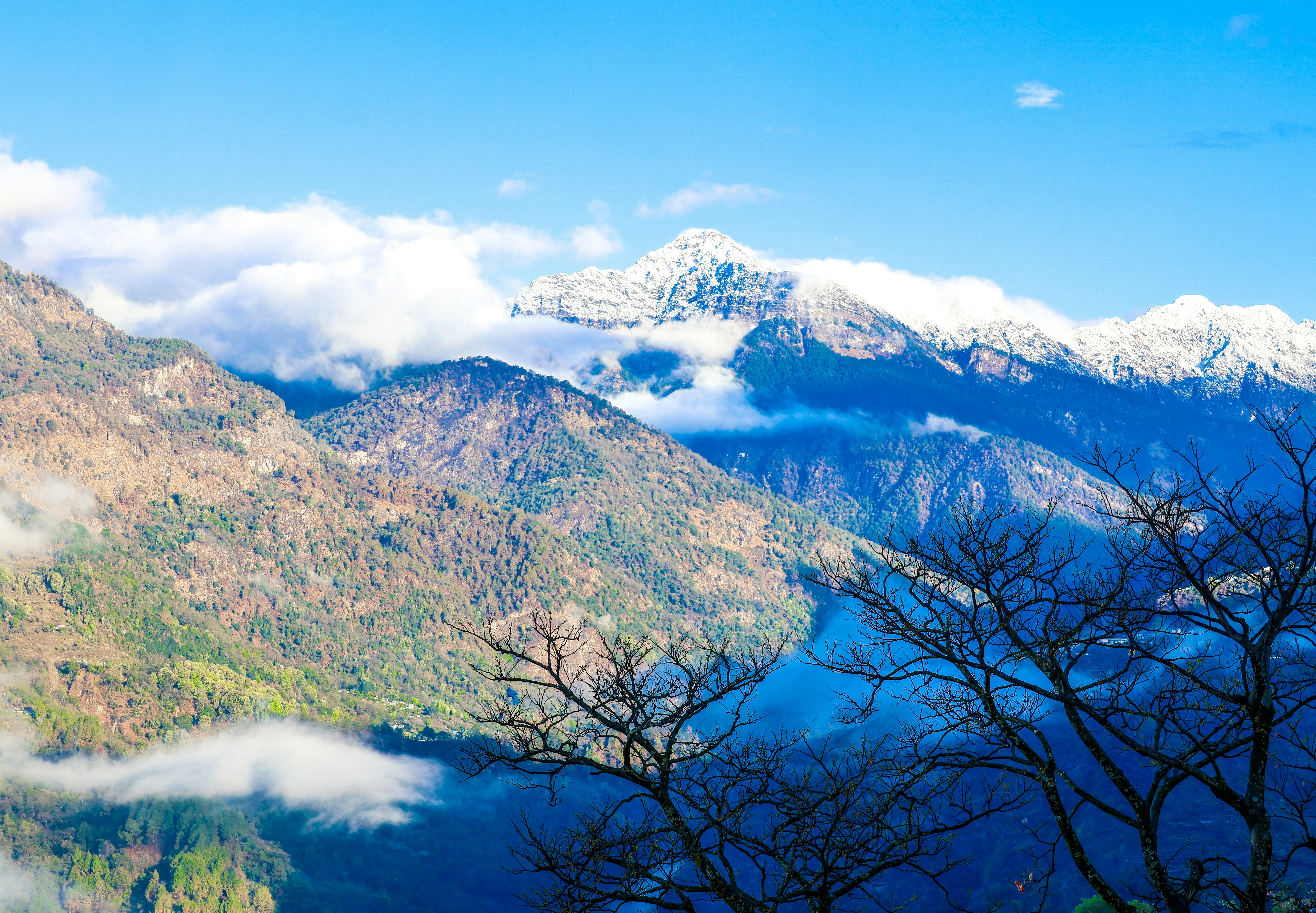Majestic snow-capped mountains with clouds under a clear blue sky.
