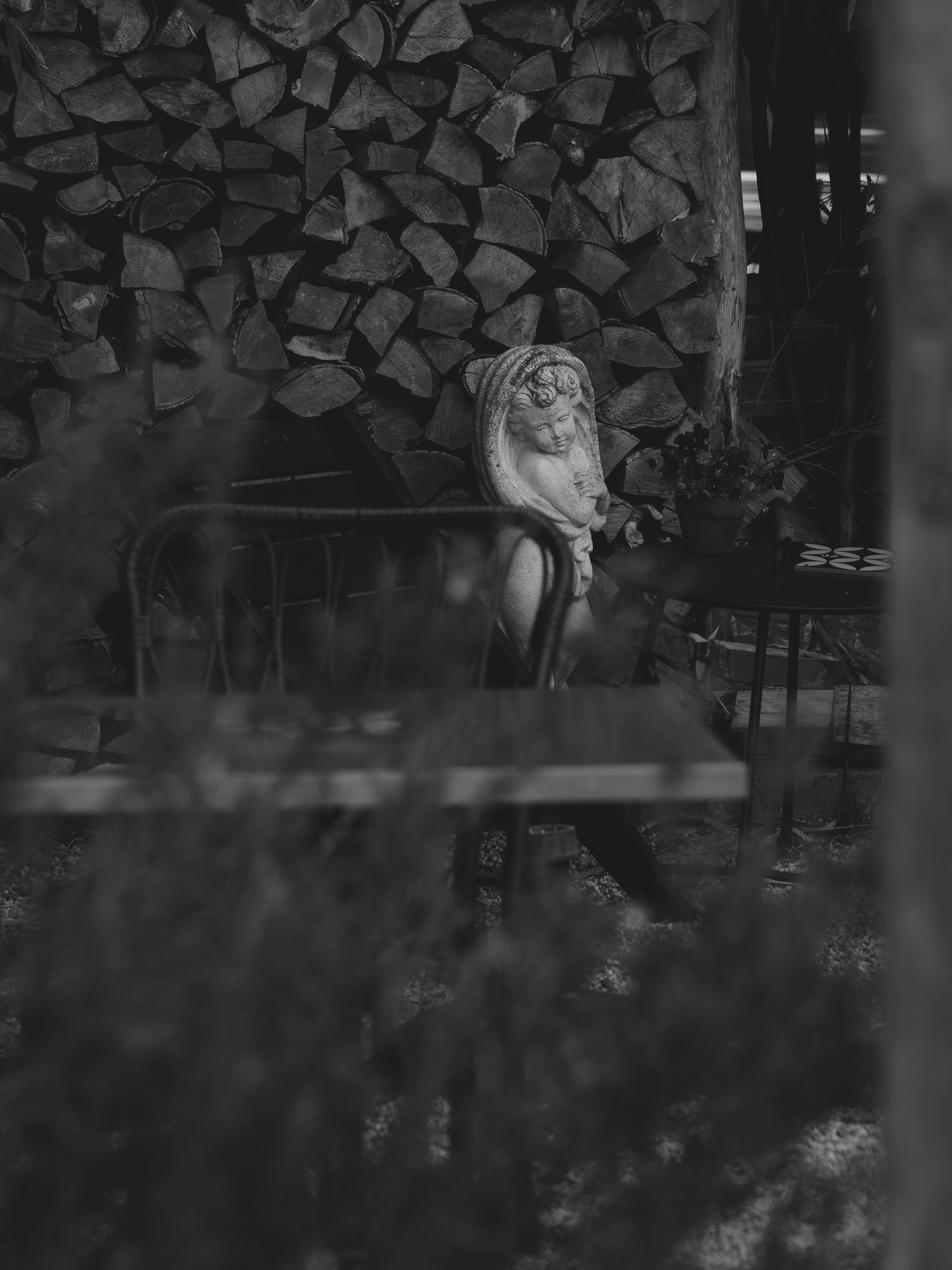Quiet Garden Shrine: Stone Angel Amid Stacked Firewood