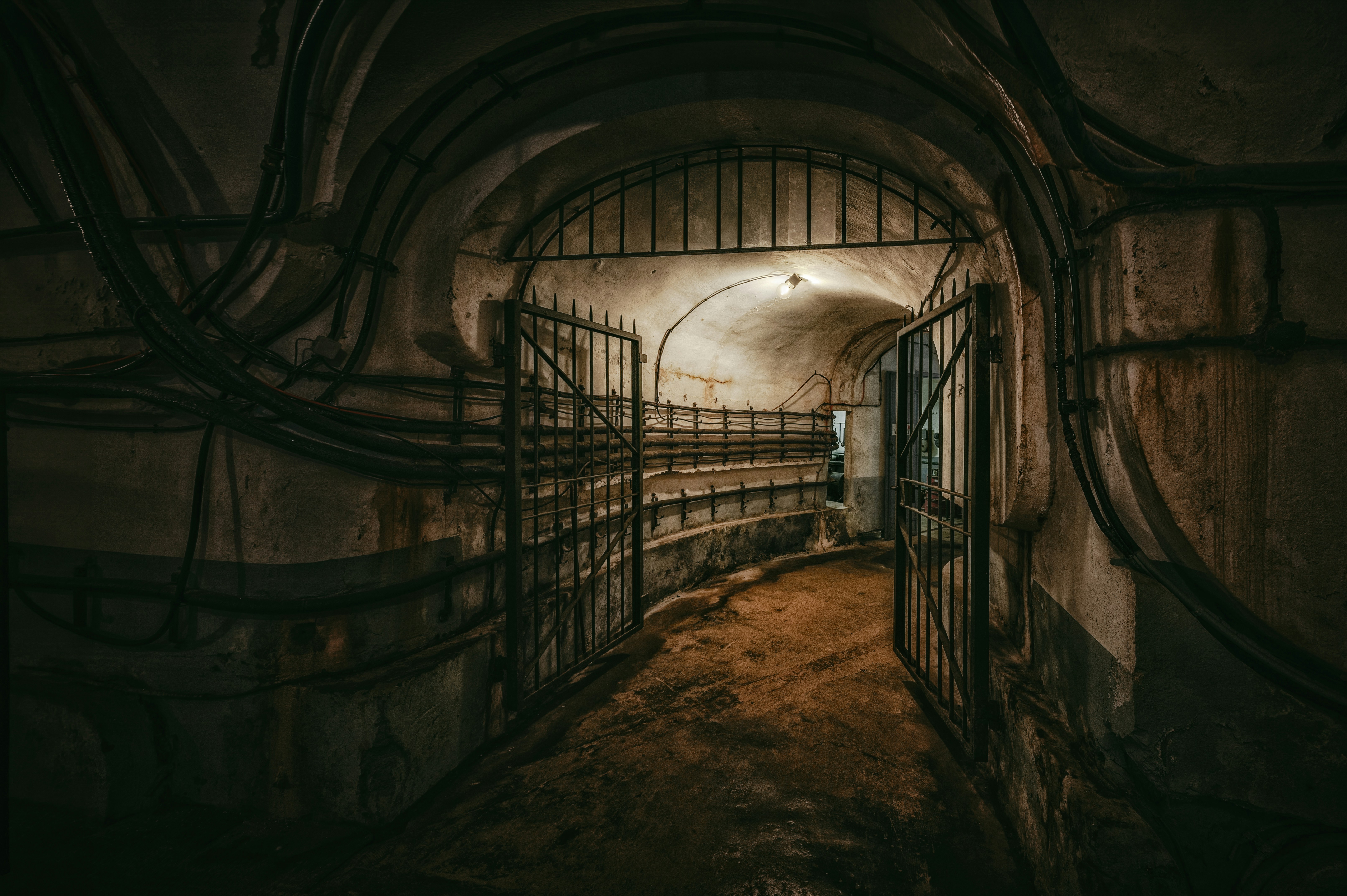 Abandoned underground bunker with arched ceiling, metal gates, and pipes.