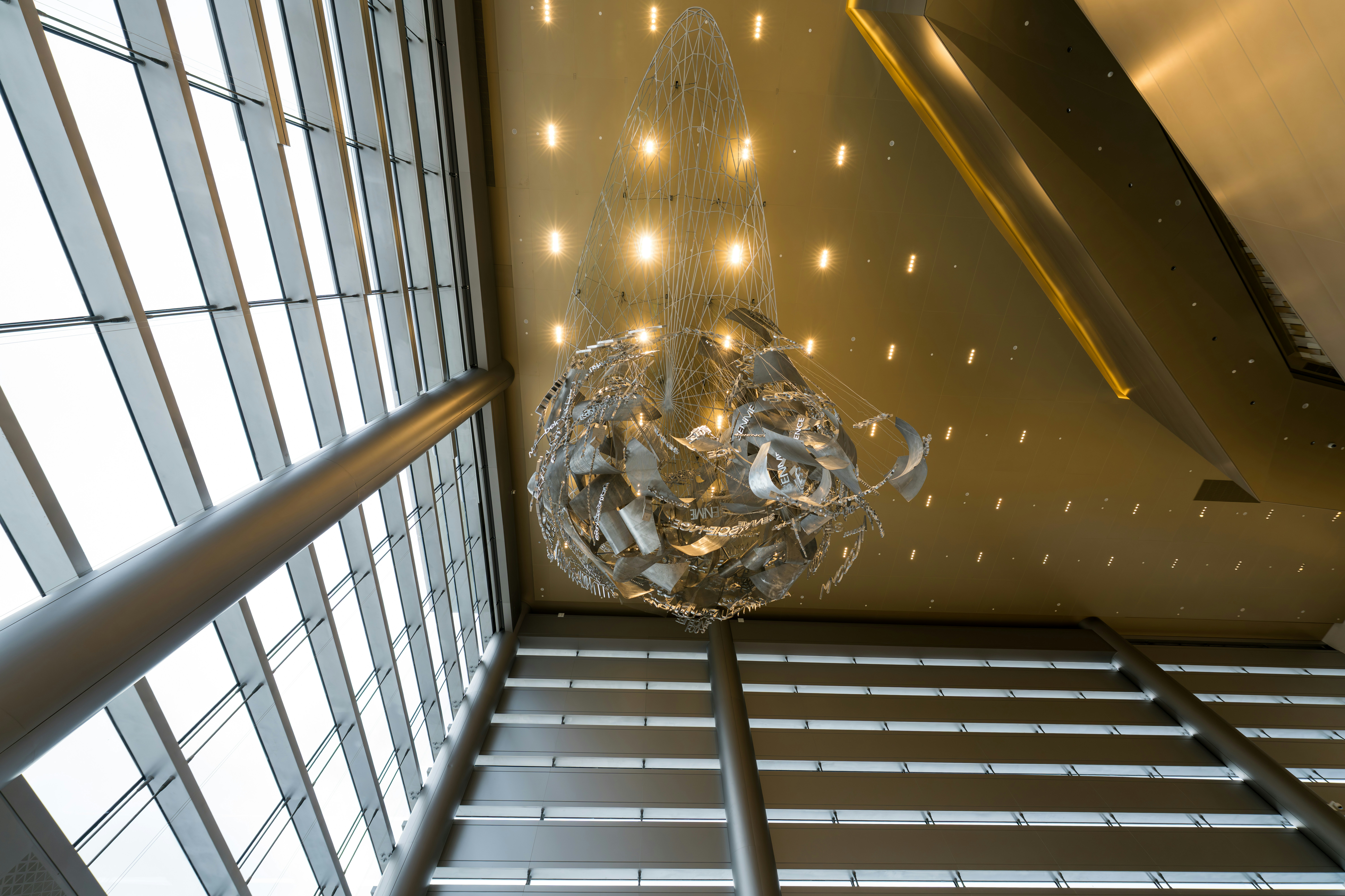 Crystal chandelier in a modern atrium suspended above a sunlit glass wall