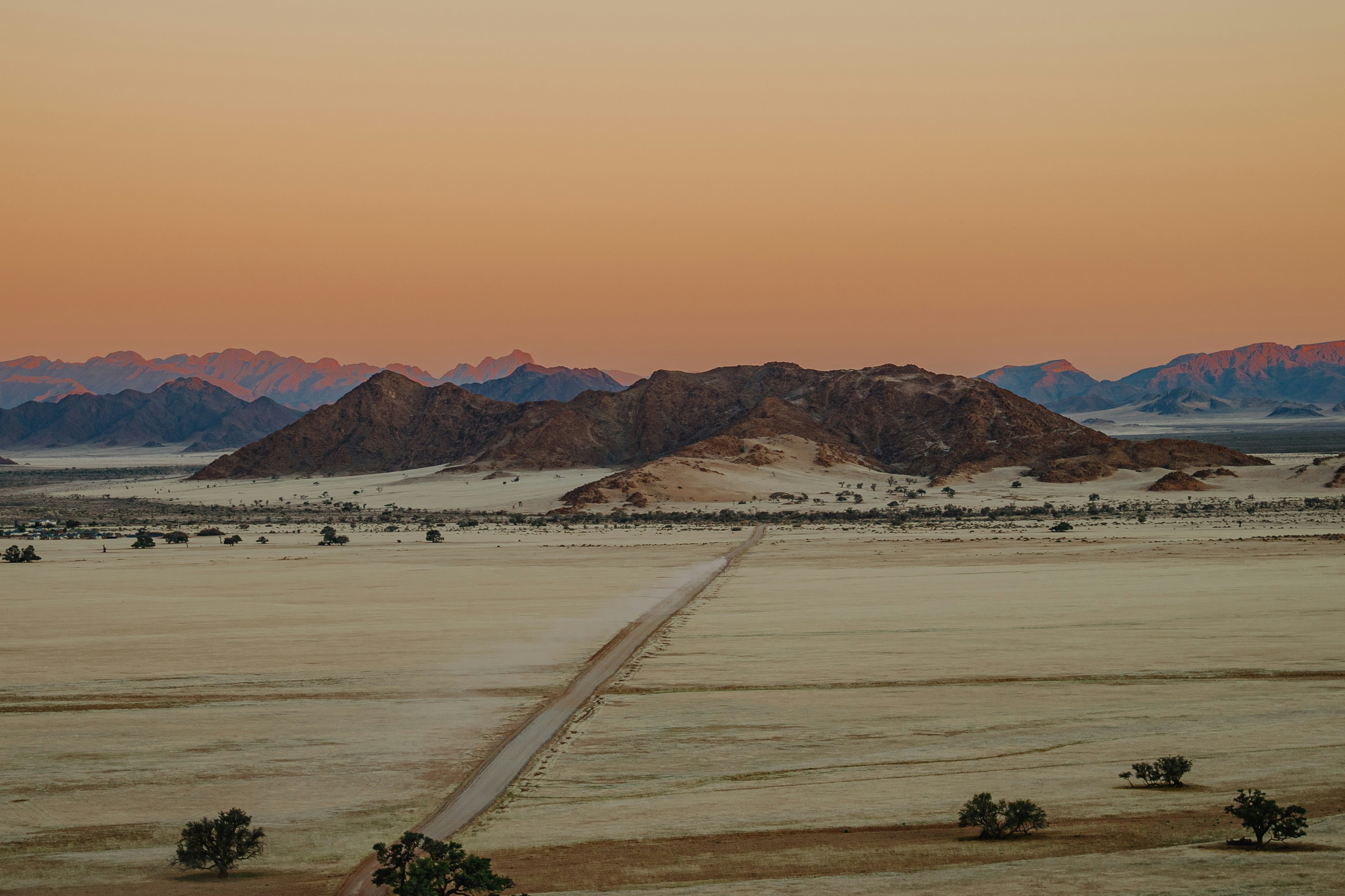 Long desert road to mountains under a vibrant sunset.