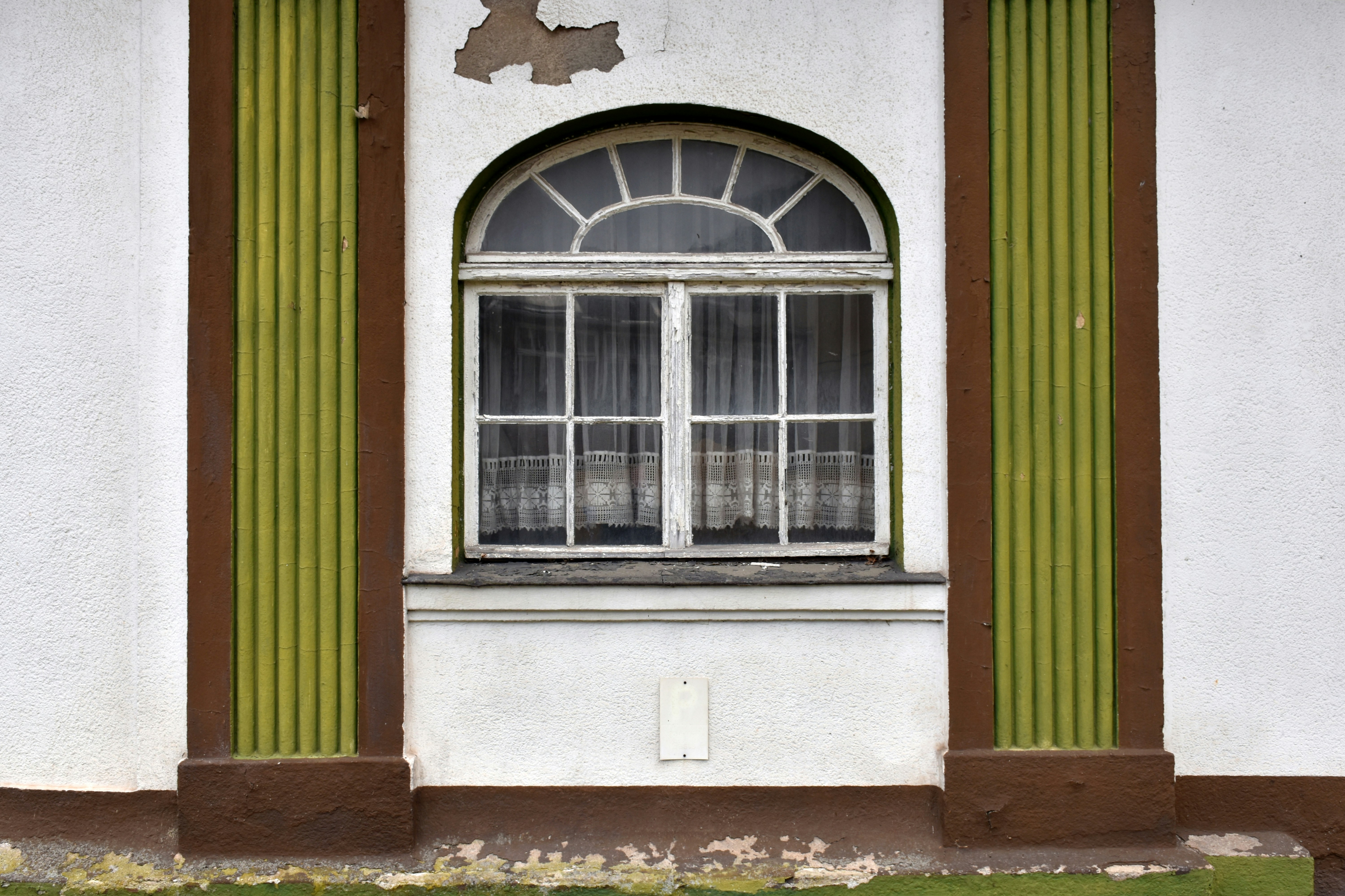 Arched Window Framed by Green Columns in Weathered Facade