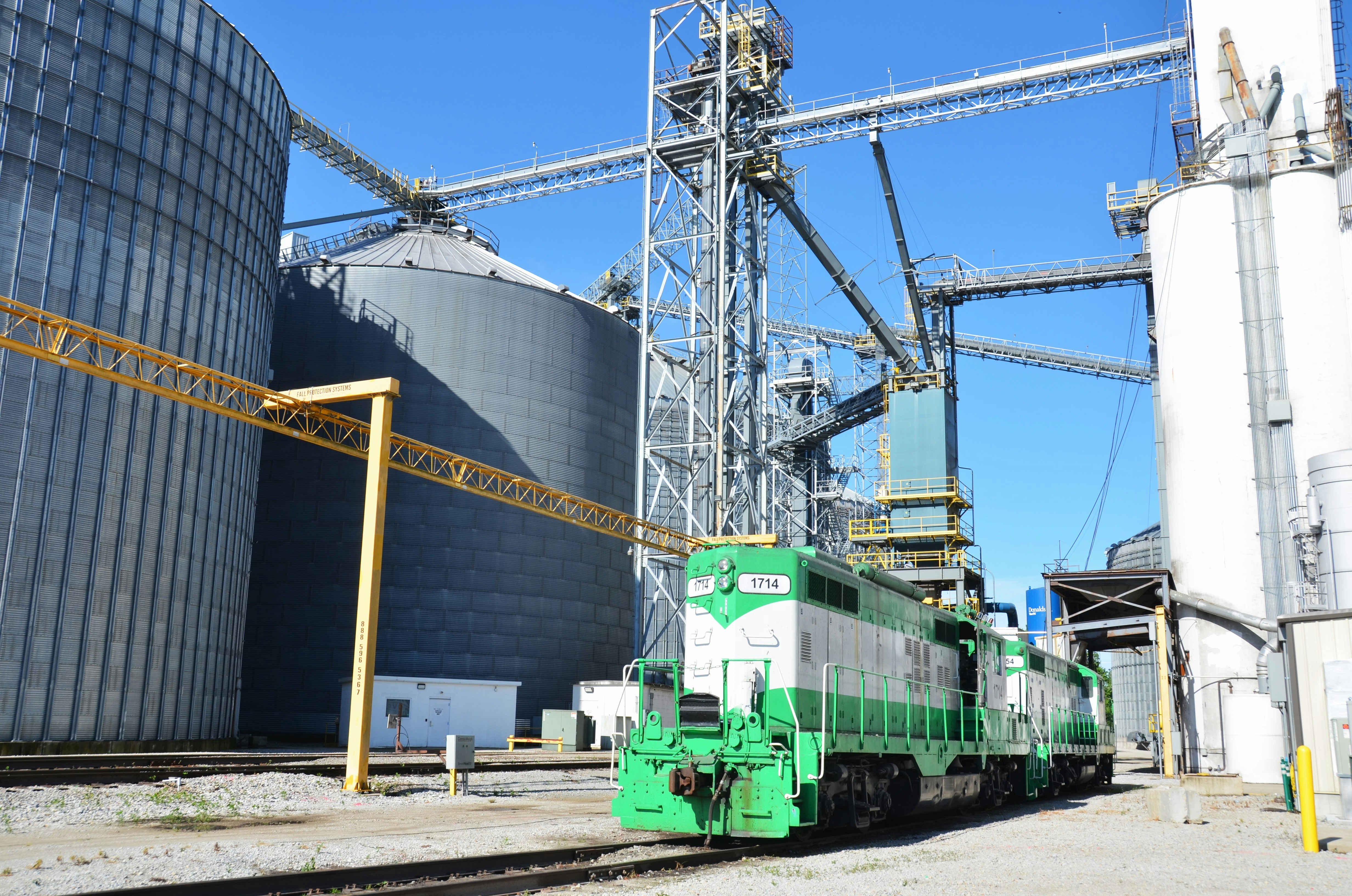 Green diesel train at industrial complex under blue sky