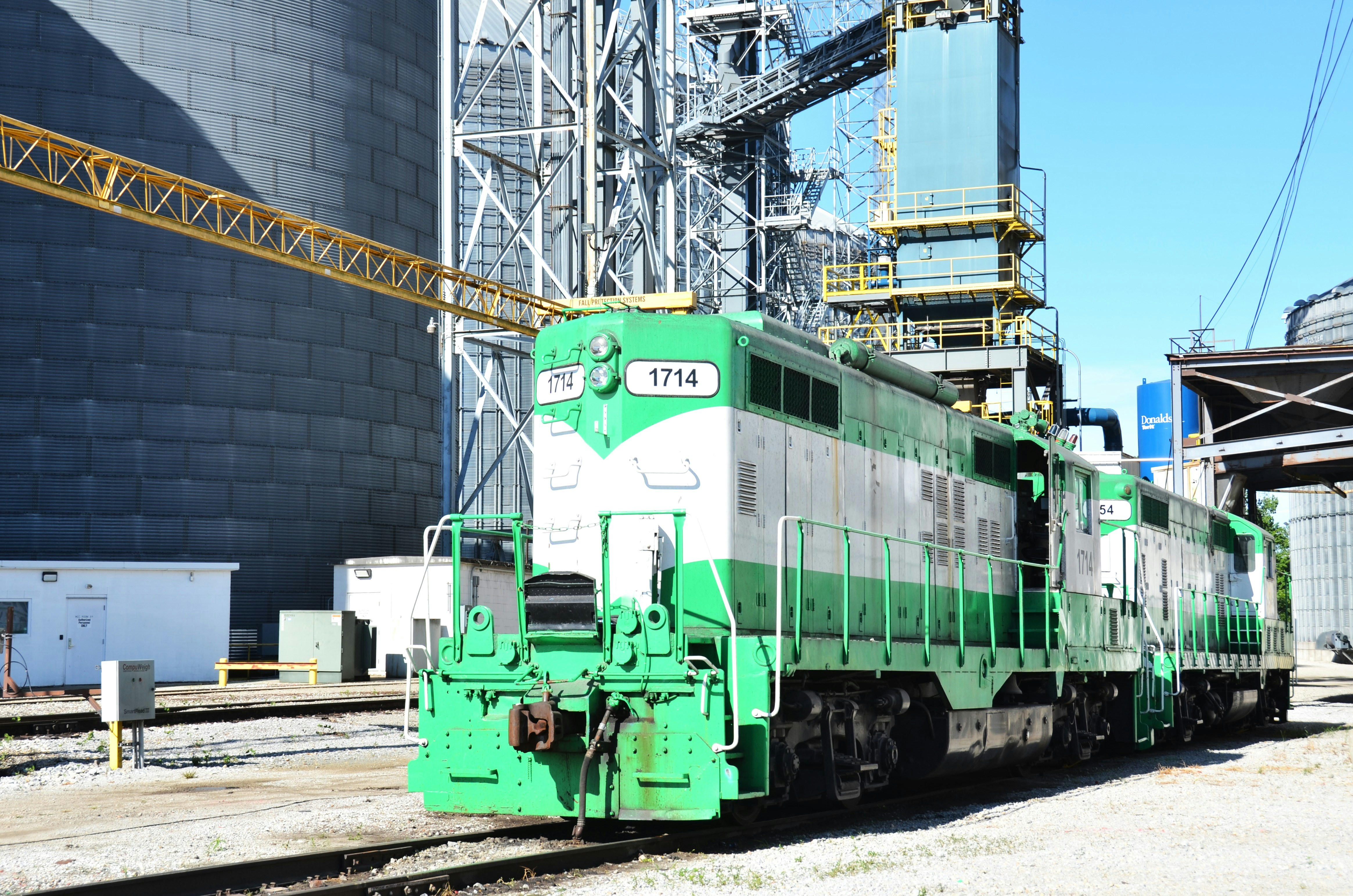 Green Locomotive at Industrial Front: A Freight Engine Under Blue Sky
