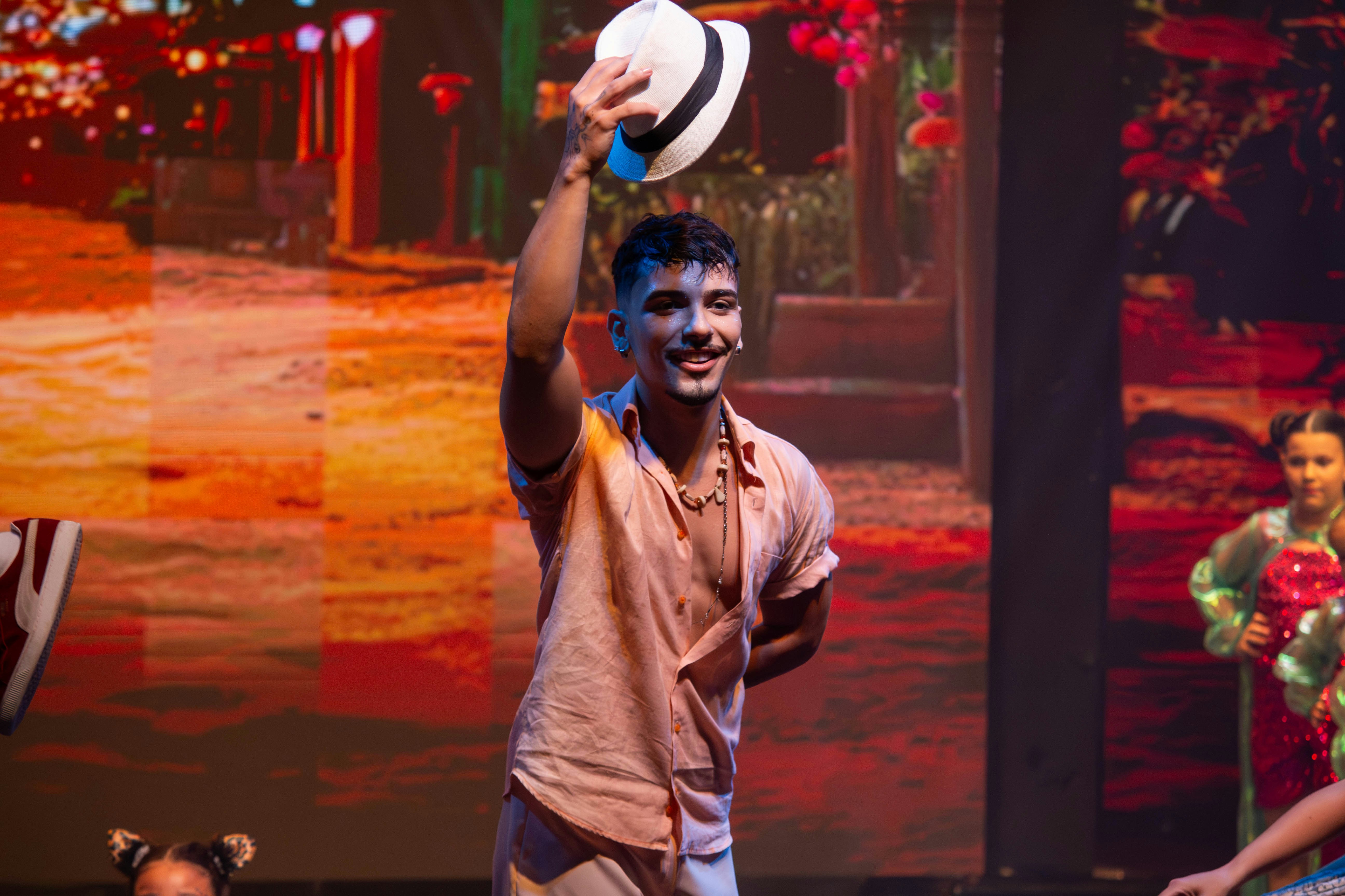 Cheerful Cape duo: A performer lifts a hat in a warm-toned stage glow
