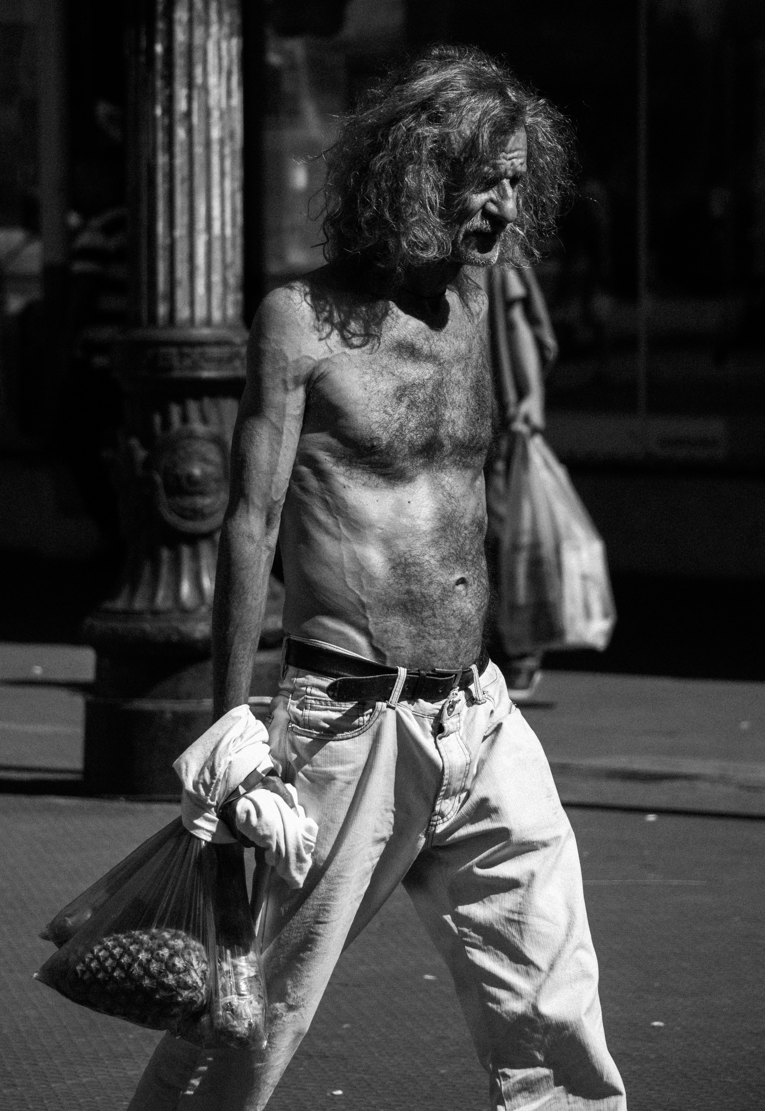 Bare-Chested Pedestrian in Sunlit Street with Grocery Bags
