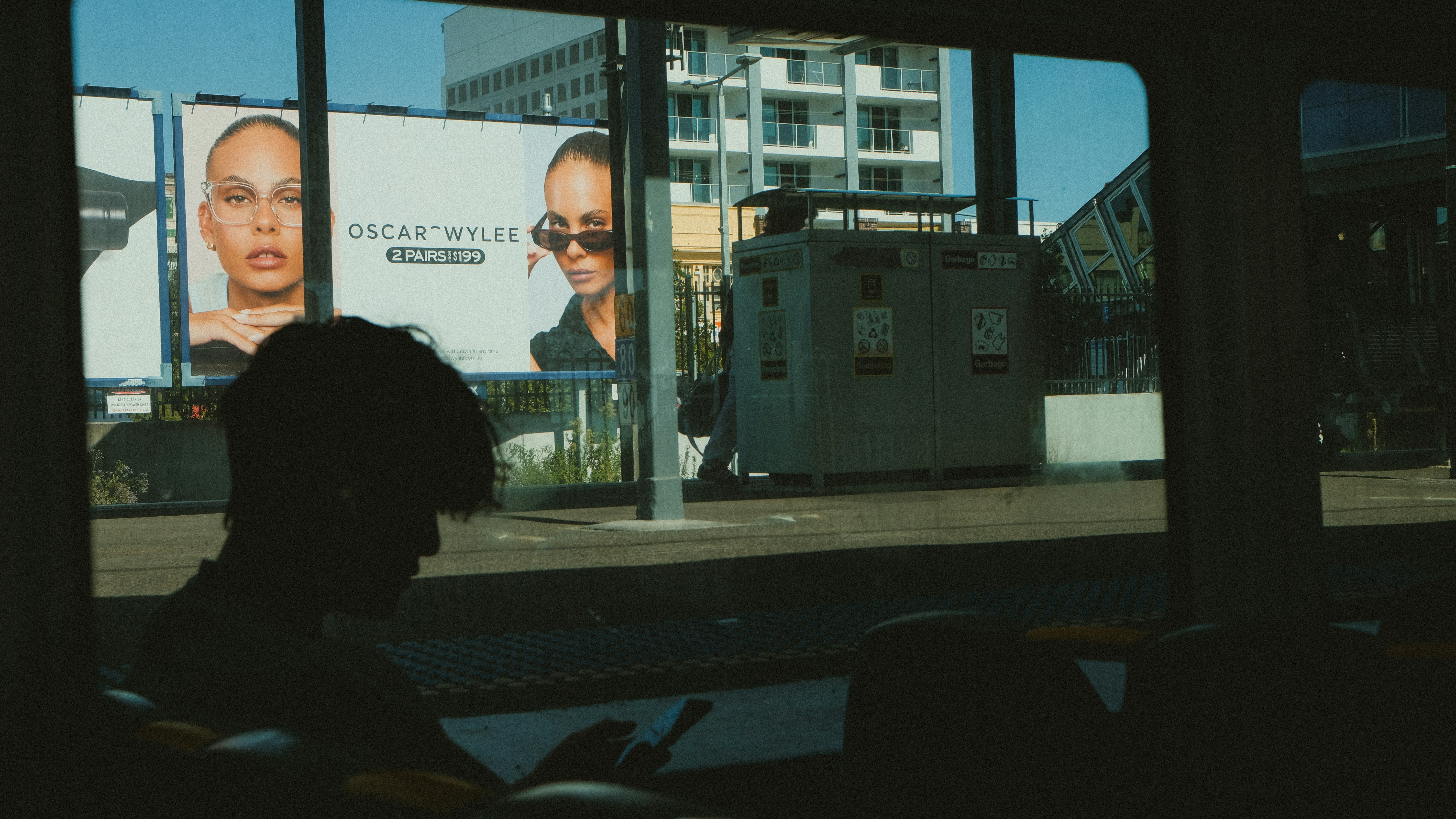 Silhouette in Transit: City Bus Window and Billboards at Dusk