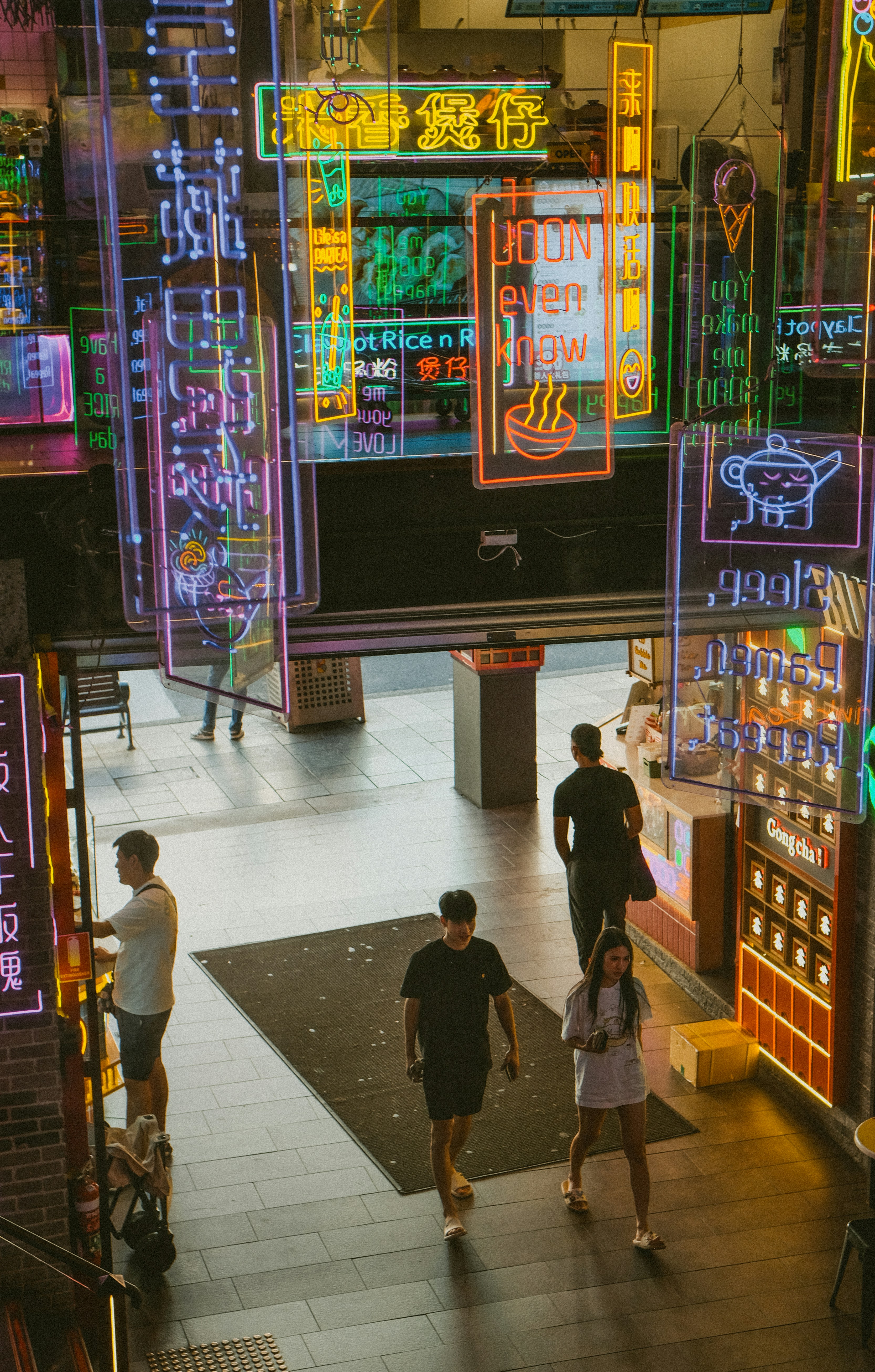 Neon Alley: People Walk Under Glowing Signage