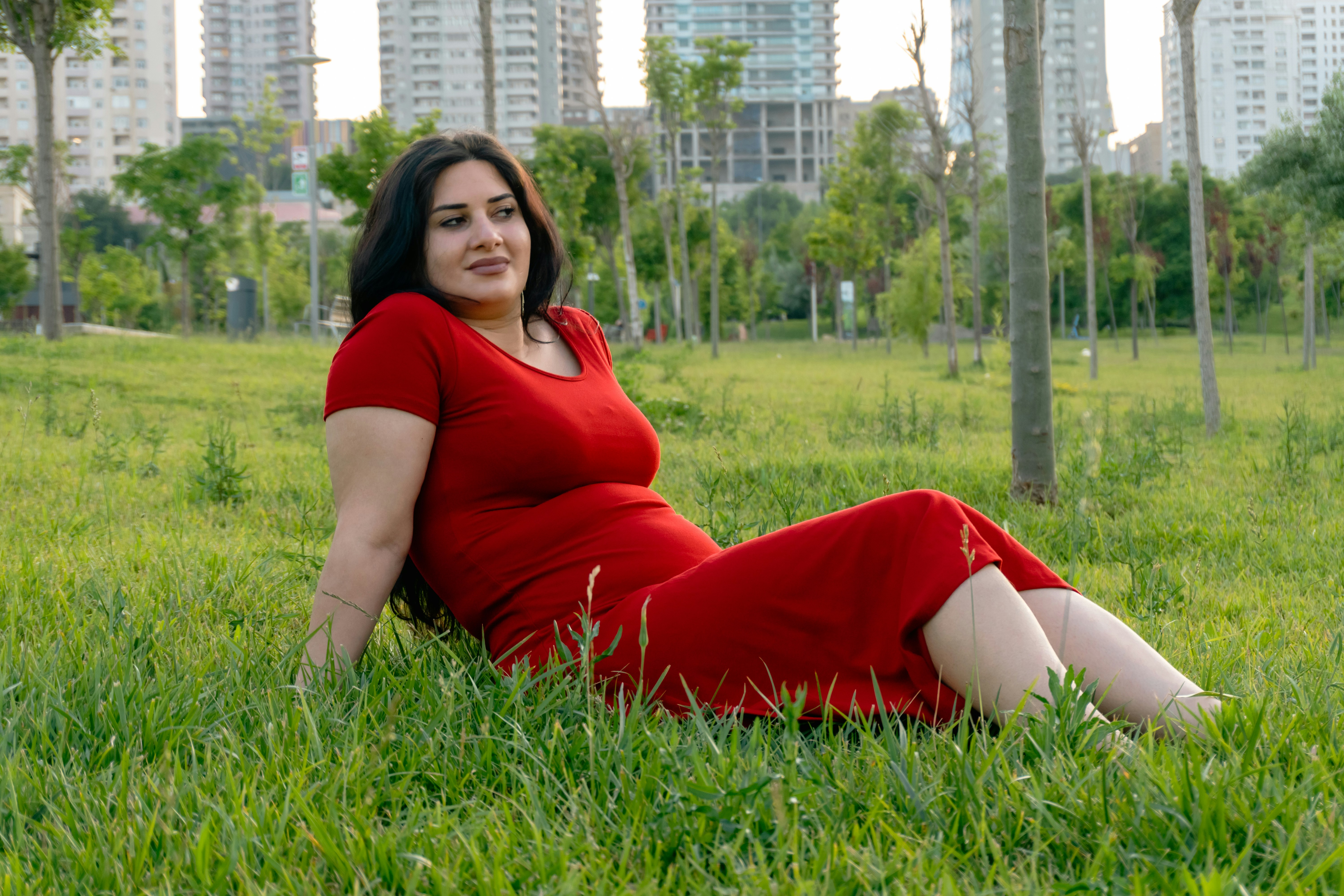 Red-dressed woman reclining on grassy field with urban skyline